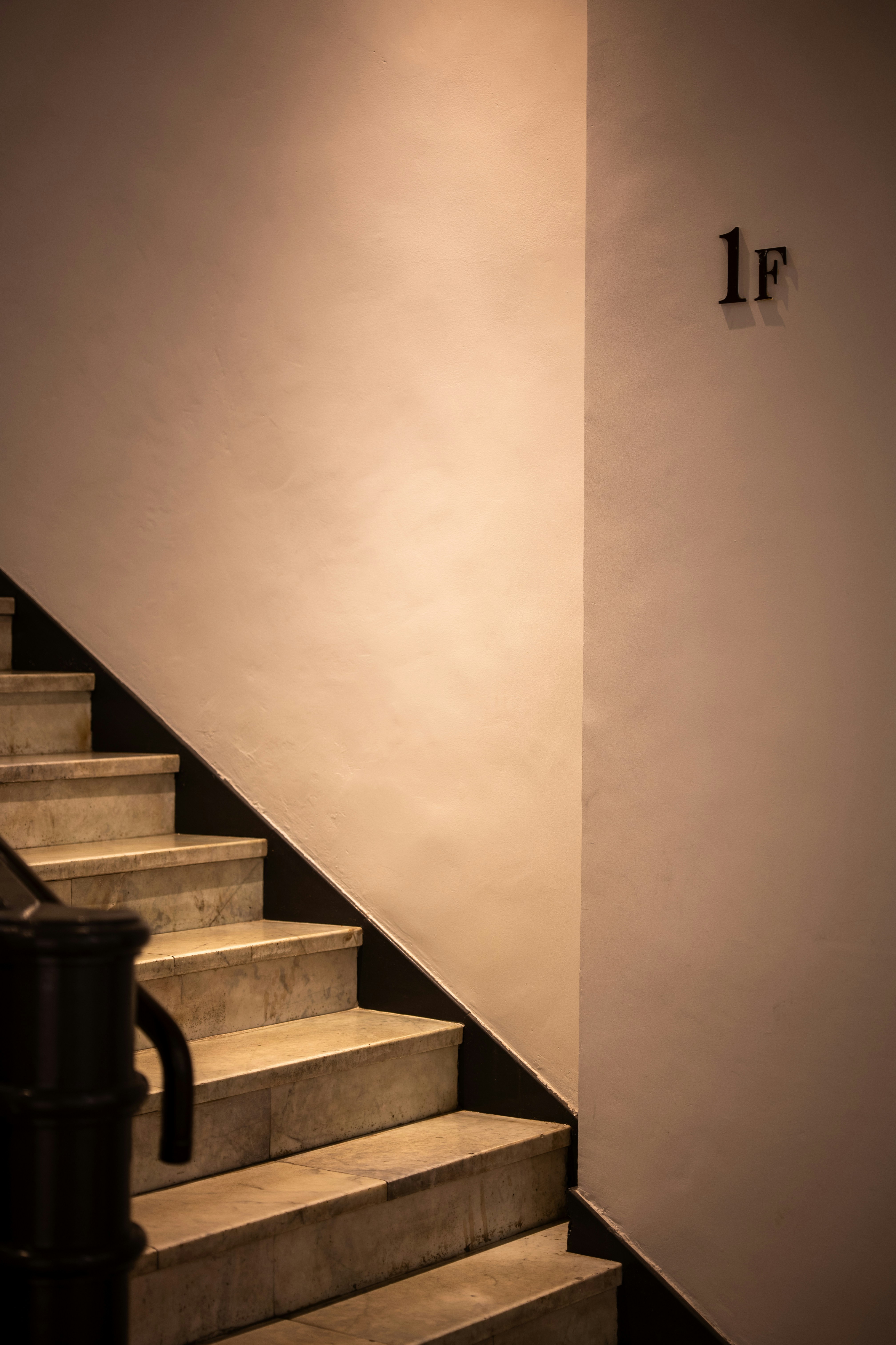 Staircase leading to the first floor, illuminated by soft light, with a minimalist design and a clear '1F' sign on the wall.