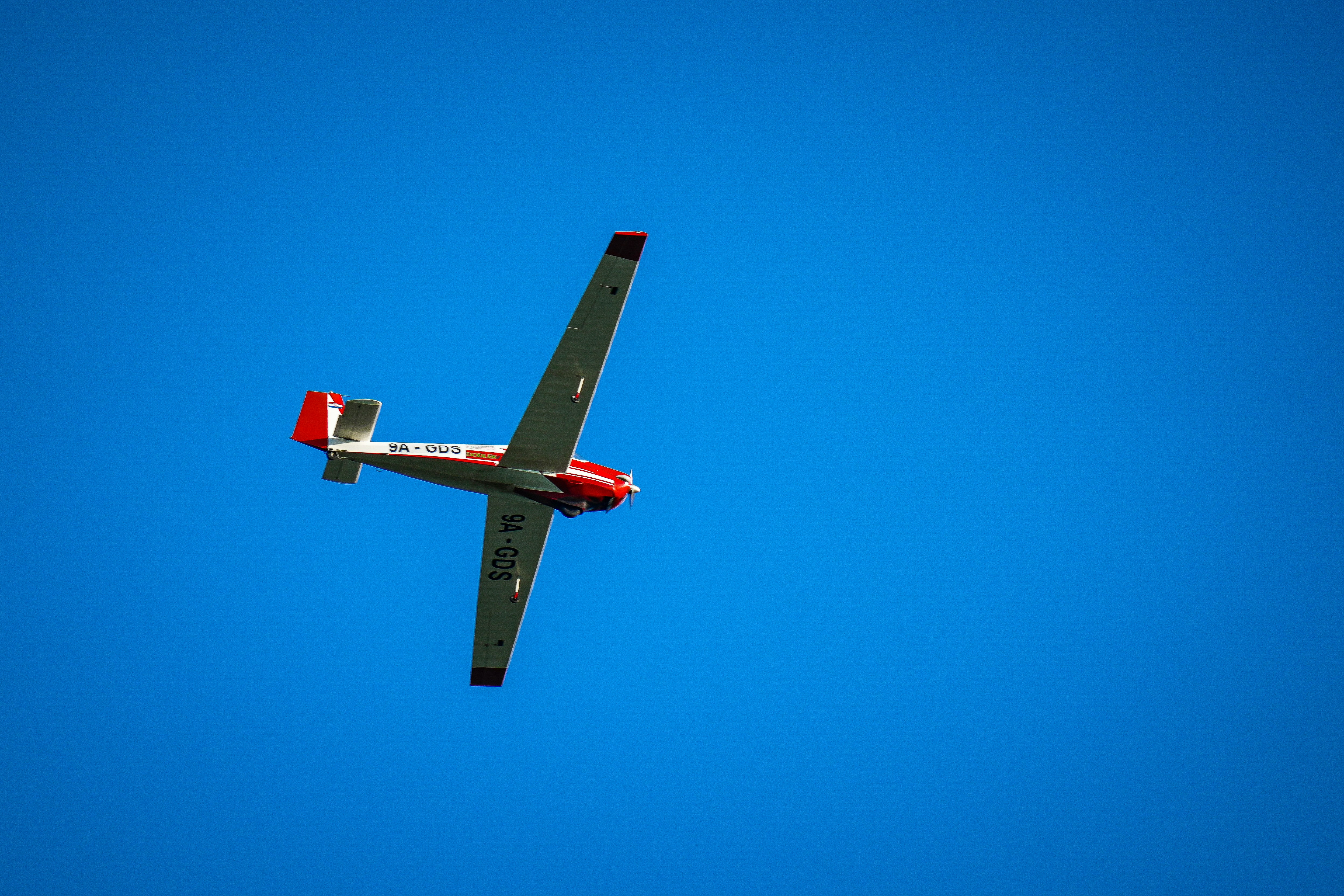 Single-engine aircraft gliding against a clear blue sky, showcasing its vibrant red and gray design.