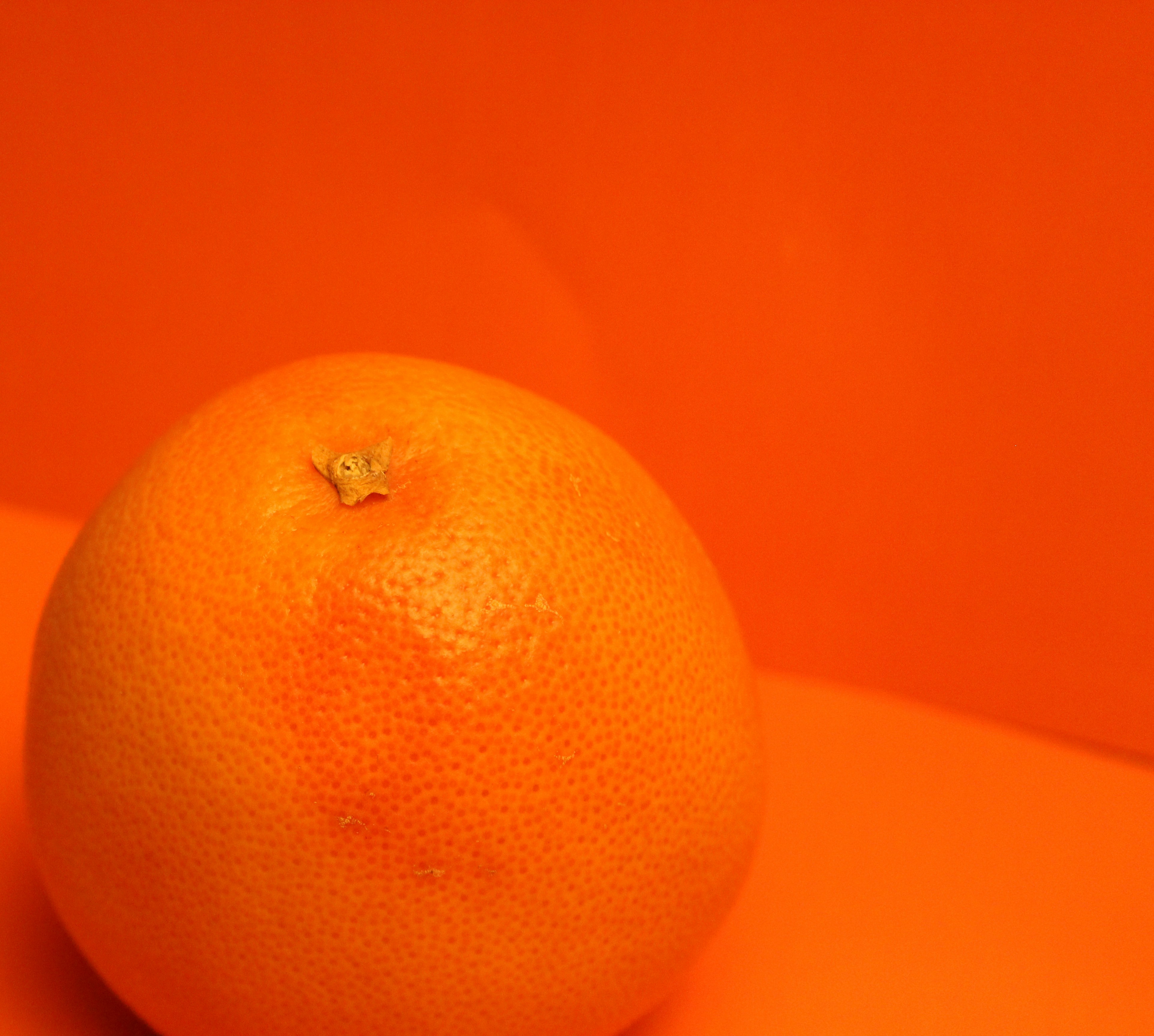 Grapefruit | An orange grapefruit sits on an orange surface.