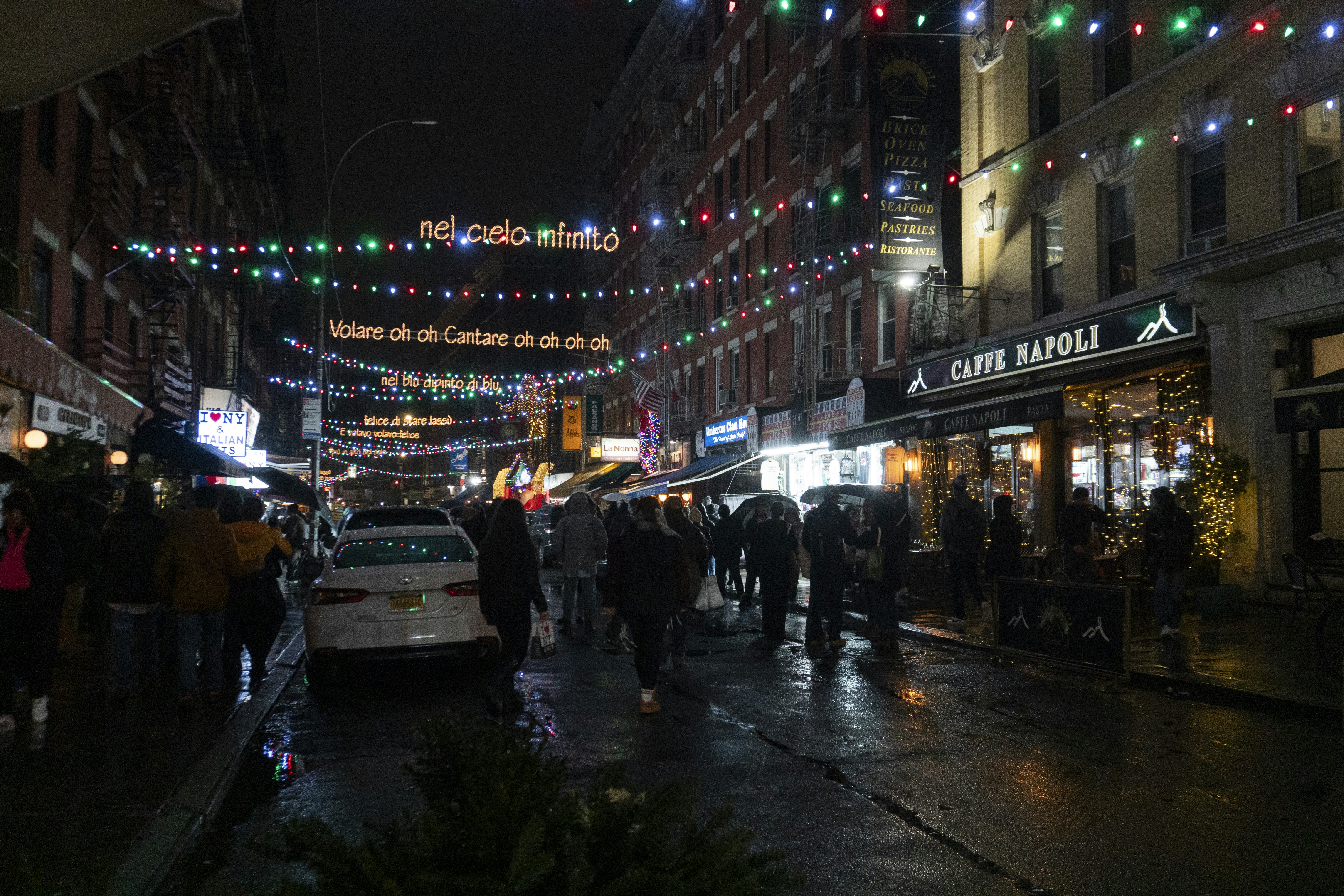 Festive street scene bustling with people, adorned with colorful lights and reflections on wet pavement.