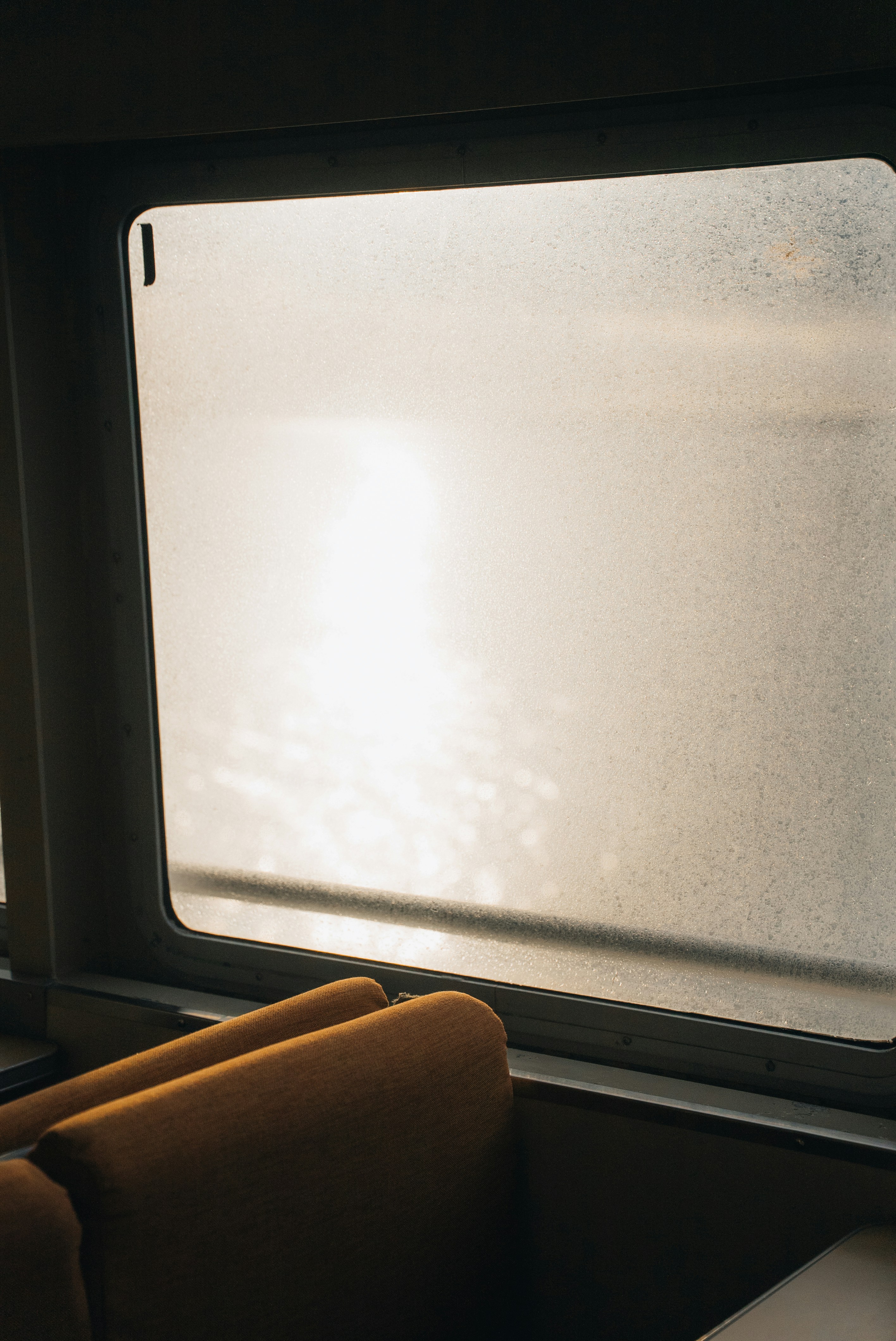 Soft reflections of sunlight on a foggy window, with a cozy seating area visible in the foreground. The scene evokes a sense of calm and contemplation.