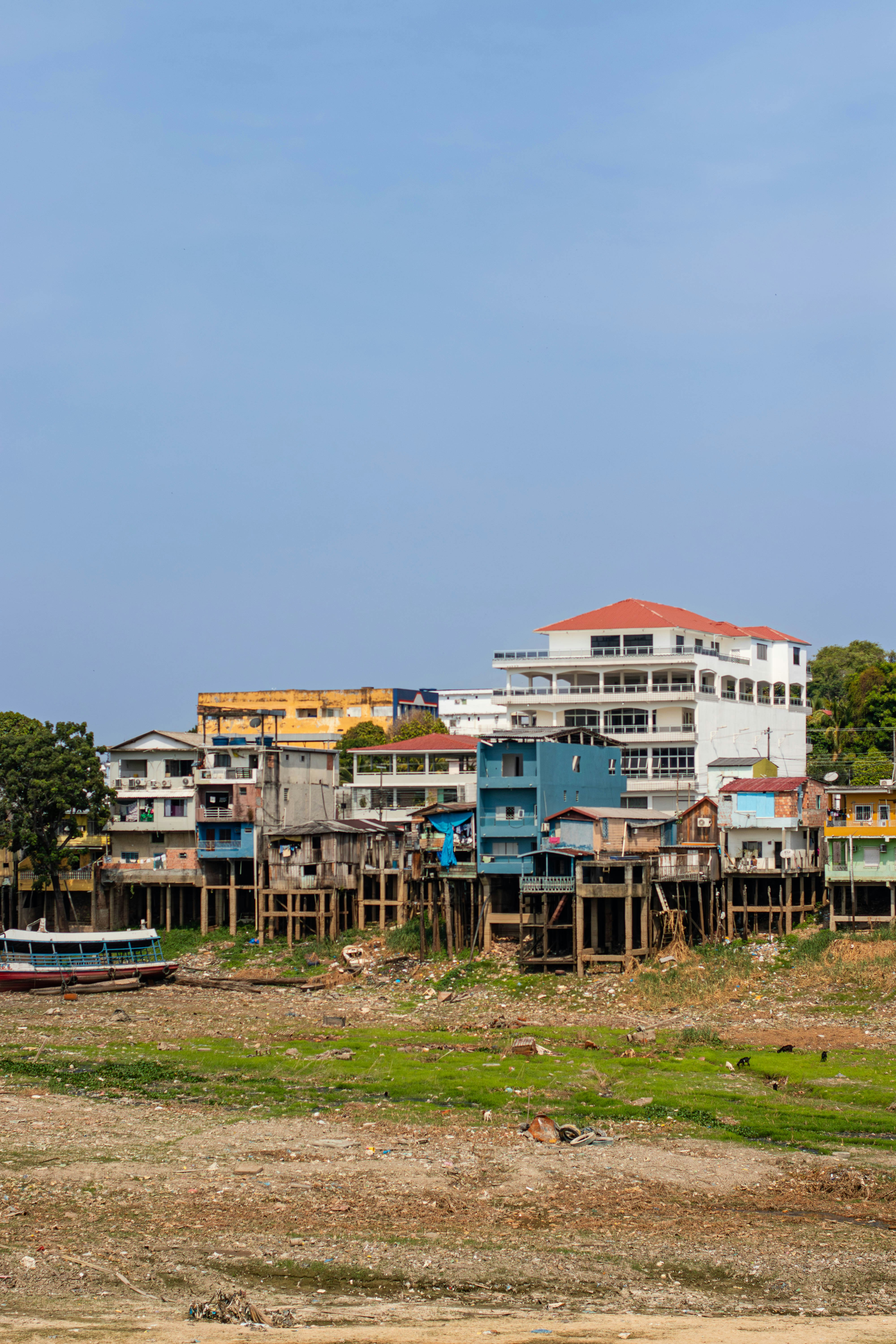 Colorful stilt houses line a riverbank, showcasing a unique architectural adaptation to coastal living amidst debris and low water levels.