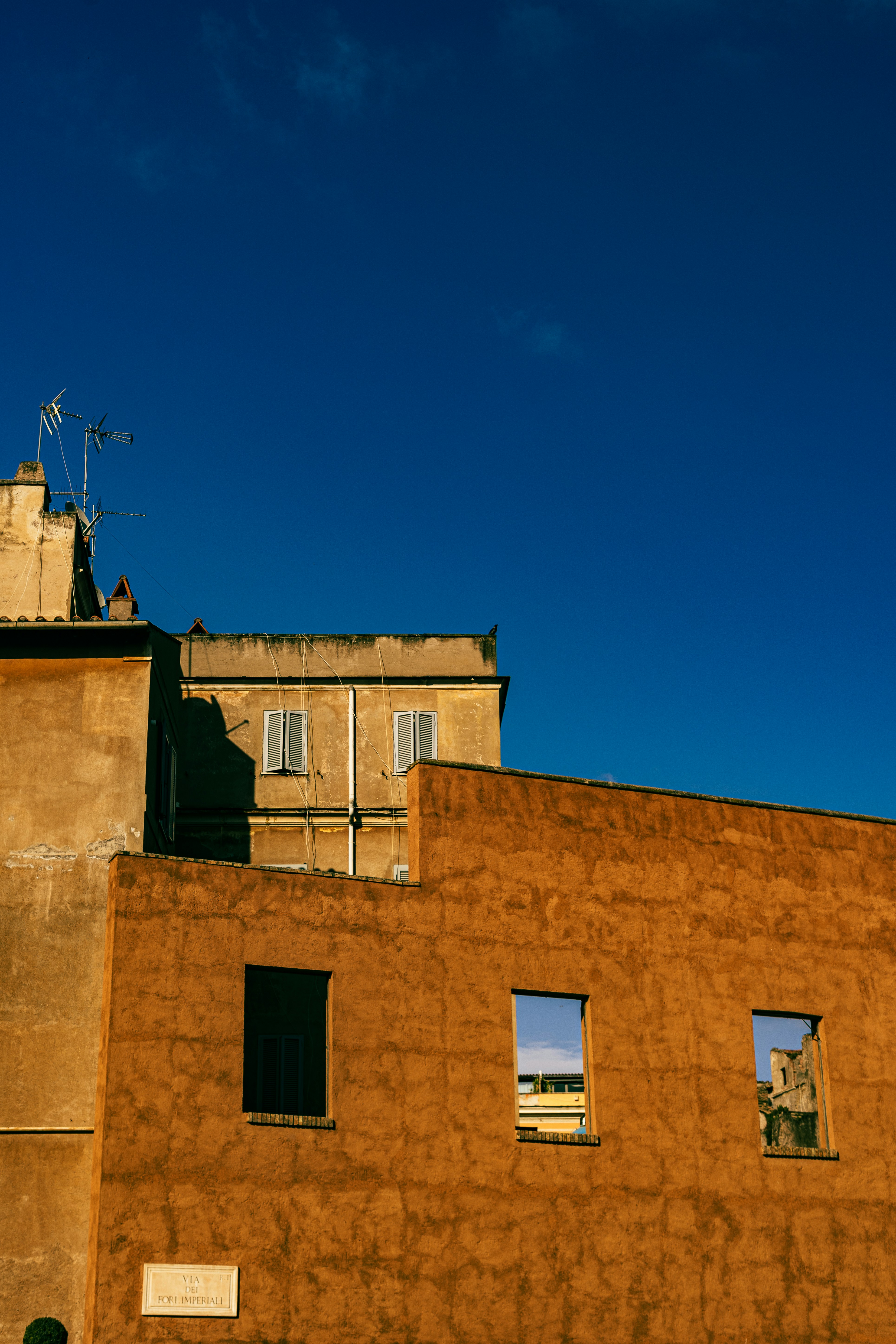 Warm-toned buildings contrast with a deep blue sky, showcasing urban architecture and a hint of daily life. The scene captures a moment of tranquility in a bustling city.