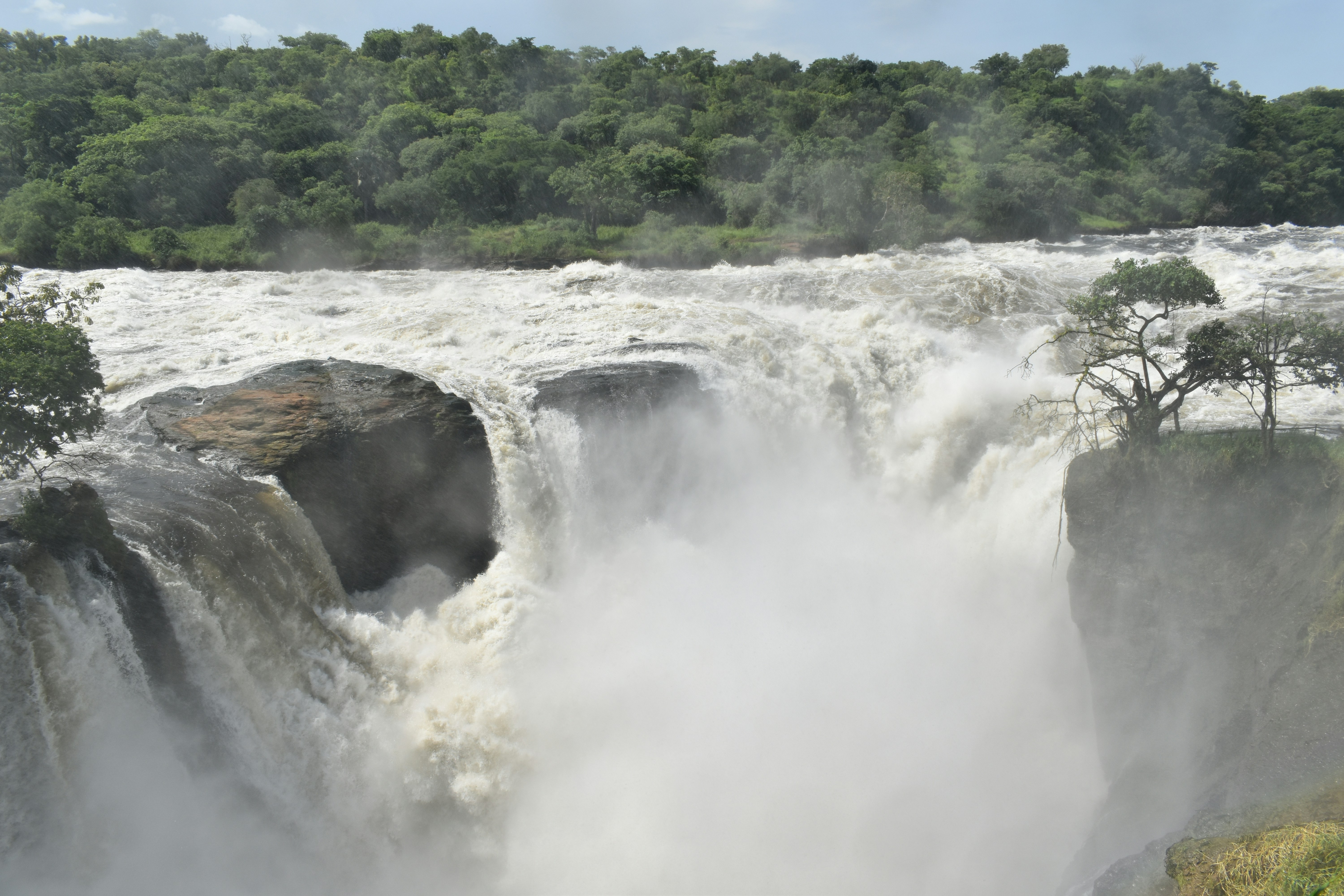 Massive waterfall cascading over rocky cliffs, surrounded by lush greenery, with mist rising from the turbulent waters.