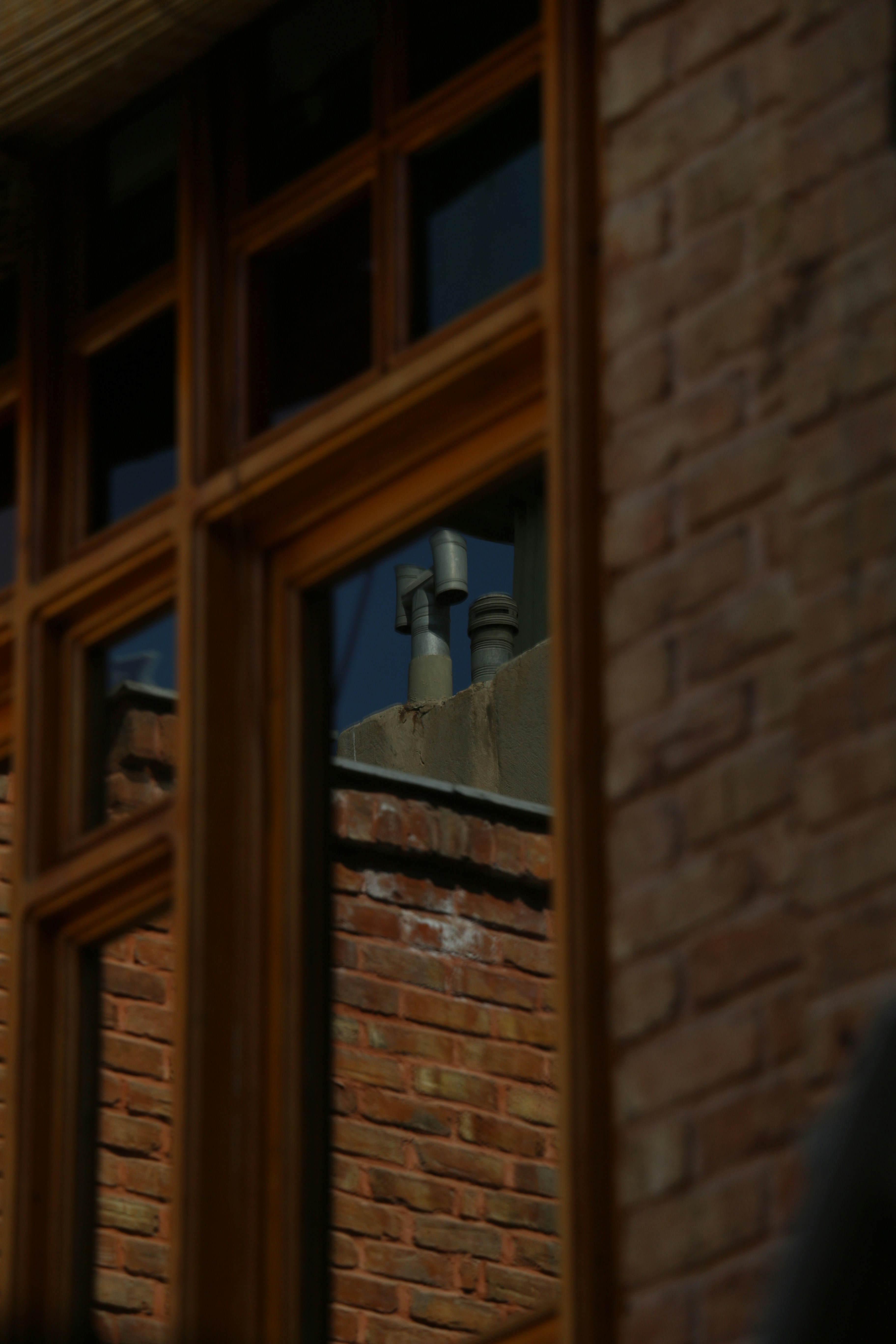Brick wall window reflections reveal factory pipes in a shallow focus, emphasizing texture and architectural detail.