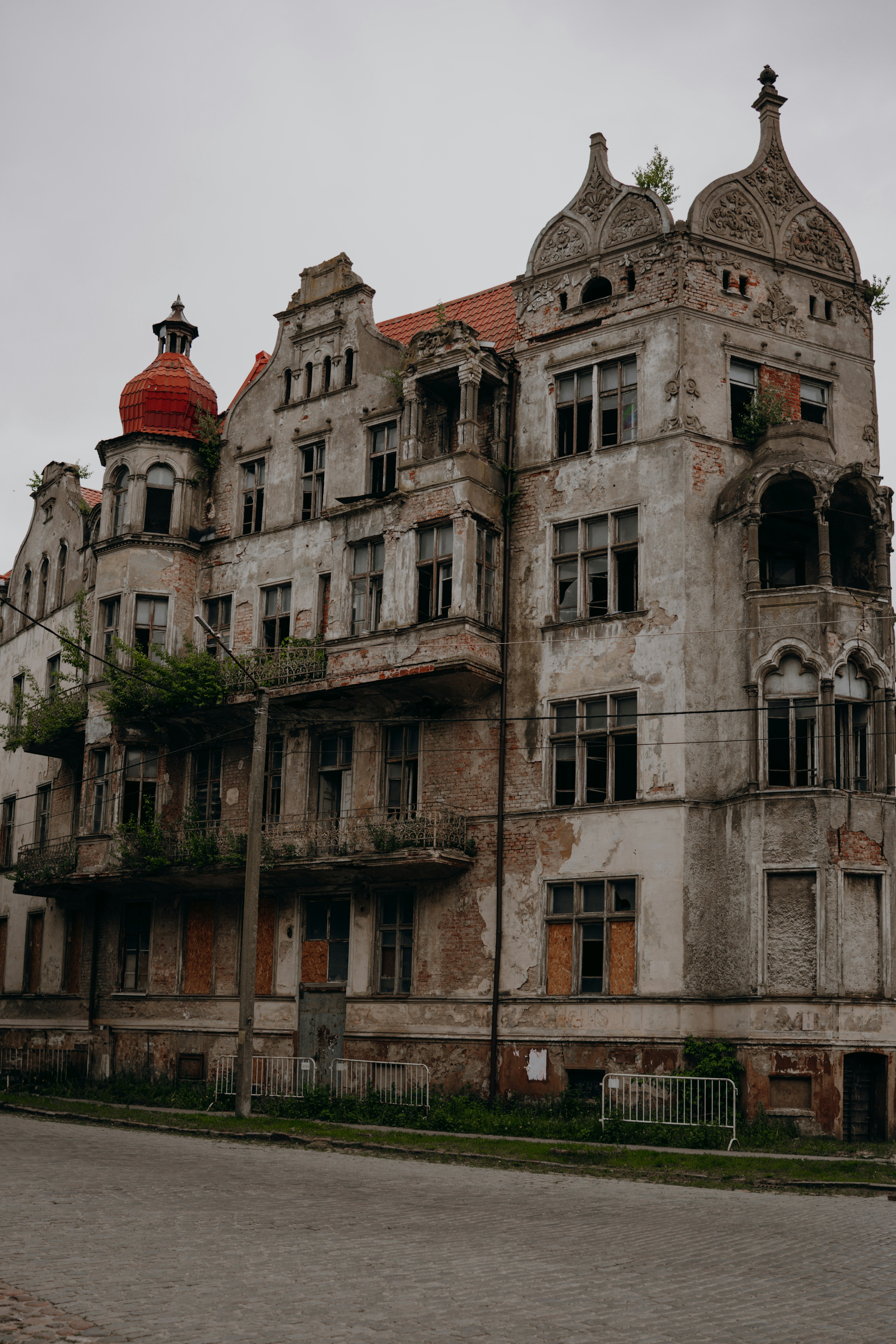 Decaying building with intricate architectural details, showcasing signs of neglect and nature's reclamation. Overgrown plants intertwine with the structure's remnants.