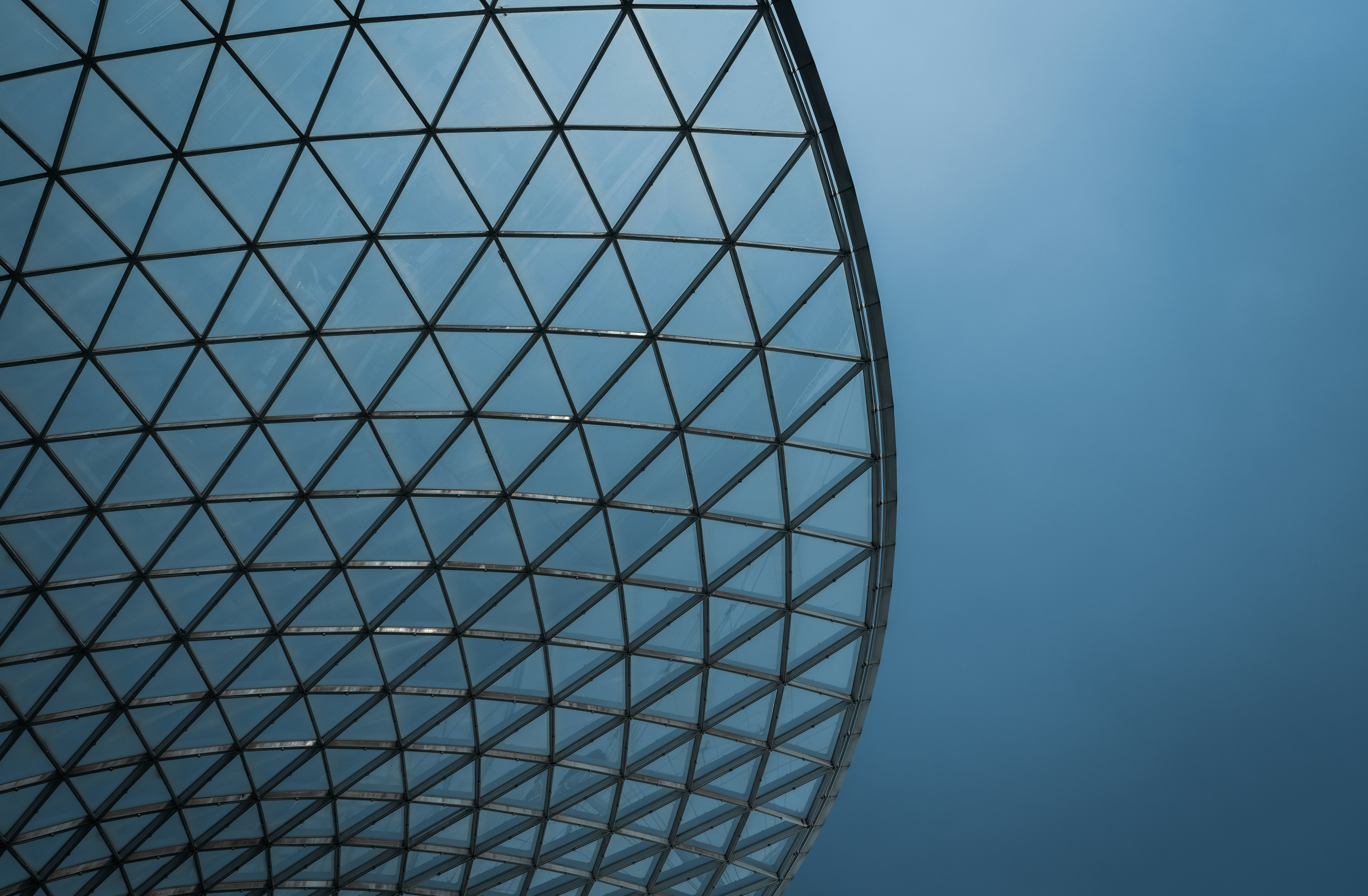 Intricate glass structure against a serene blue sky, showcasing modern architectural design.