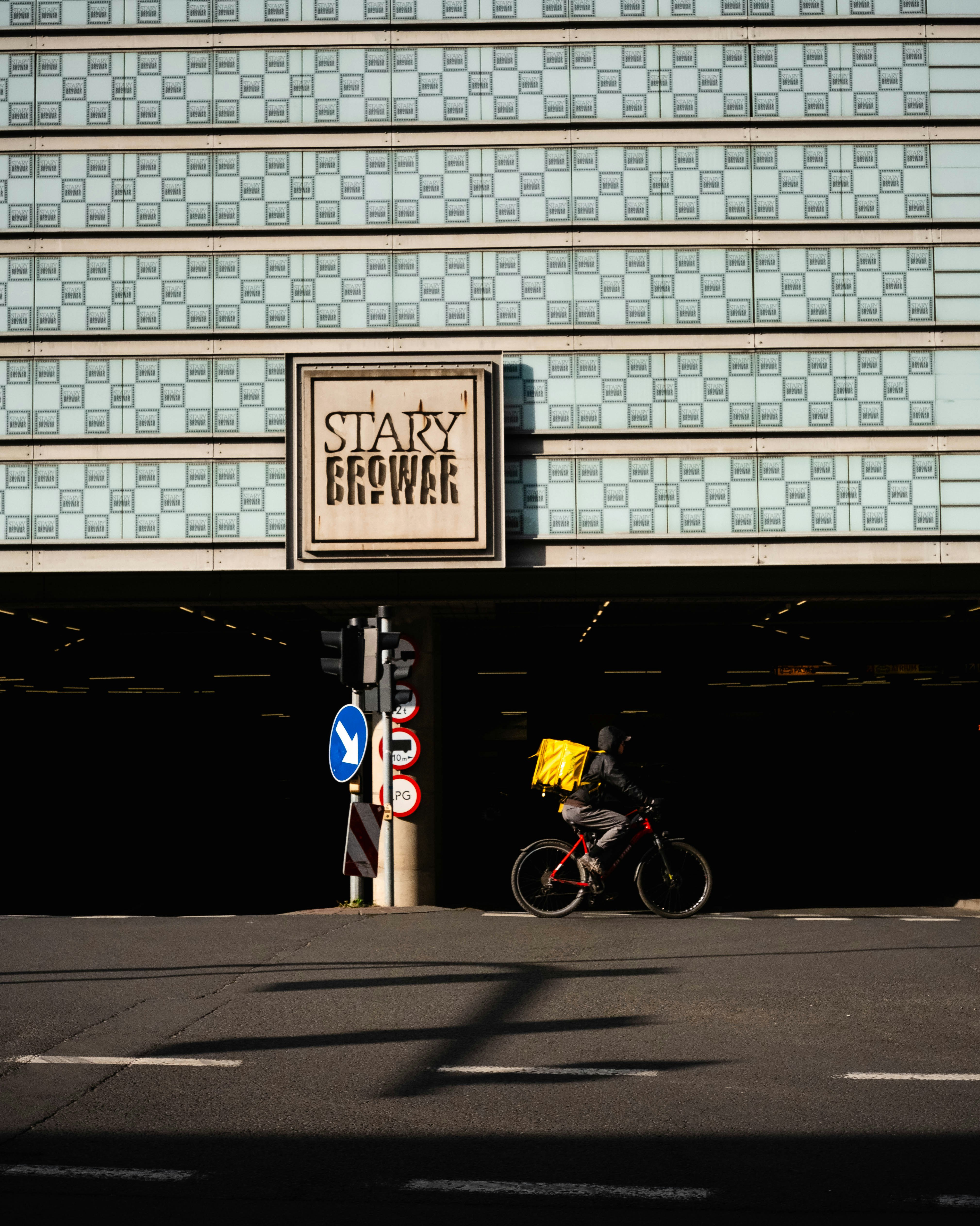A cyclist navigates the urban landscape, passing by a modern building adorned with a prominent logo. The scene captures the essence of city life and movement.