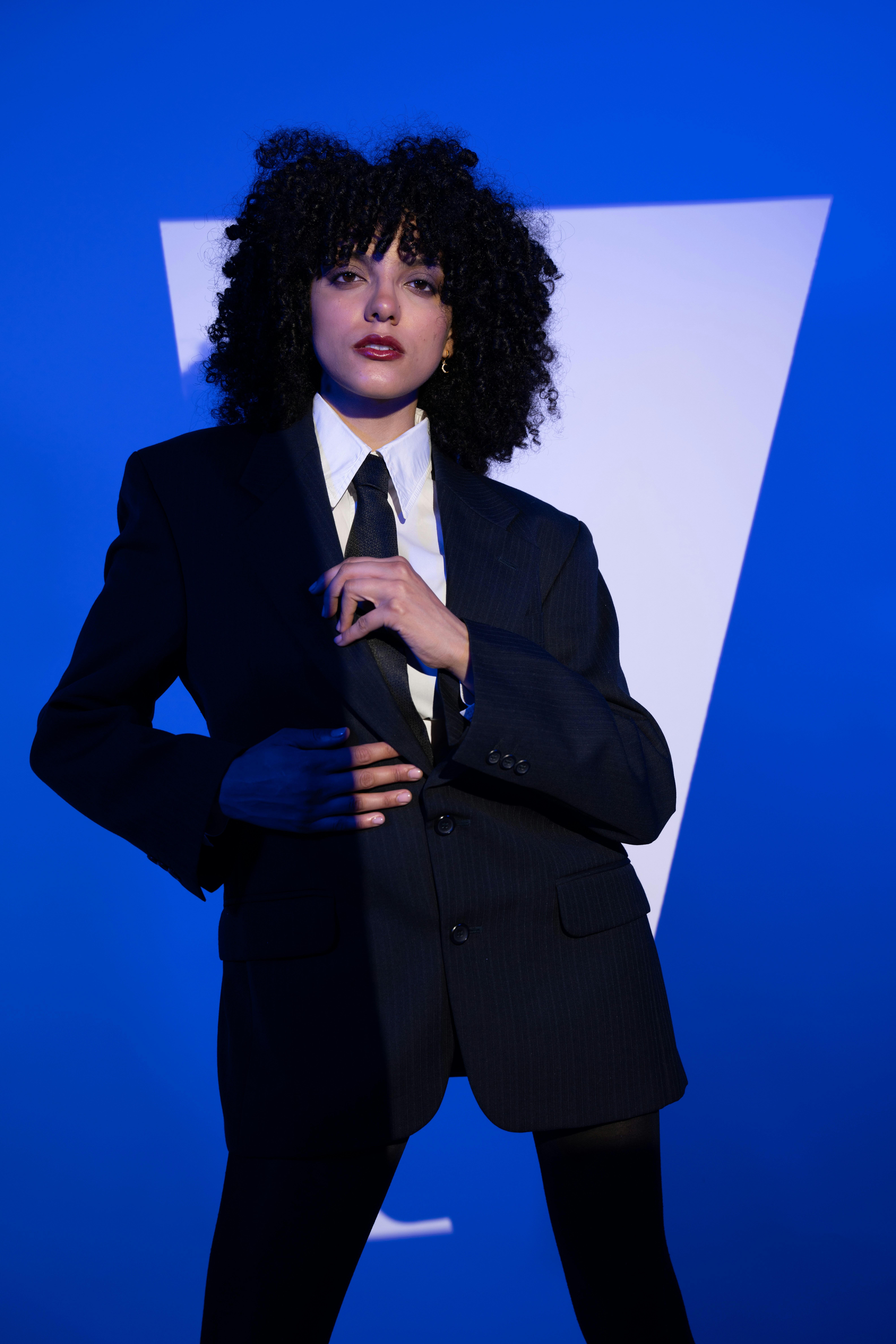 A fashion-forward individual poses confidently in a tailored suit against a vibrant blue backdrop, showcasing a blend of contemporary style and classic elements.