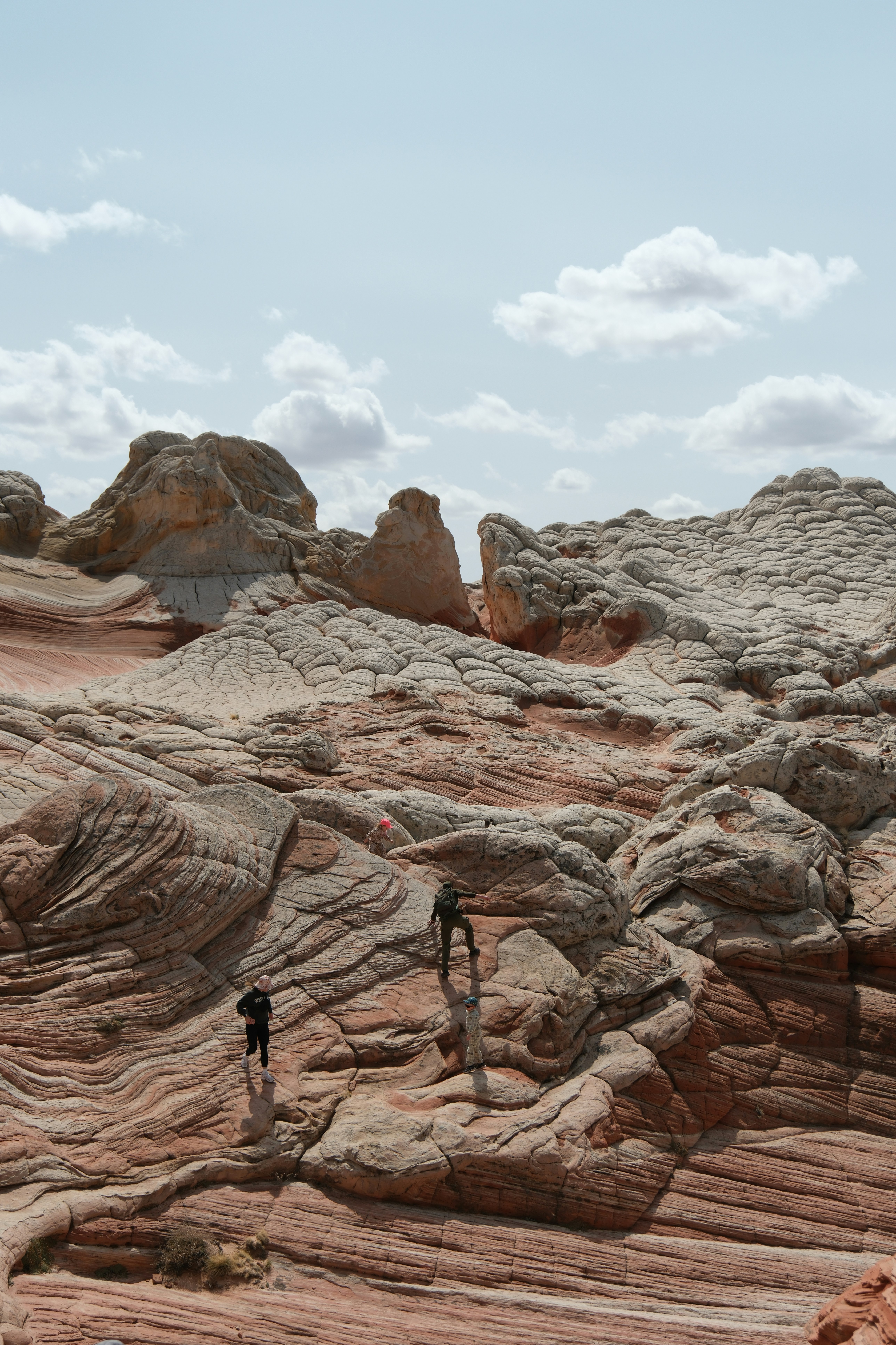 Two climbers navigating the textured, colorful rock formations of a desert landscape under a cloudy sky.