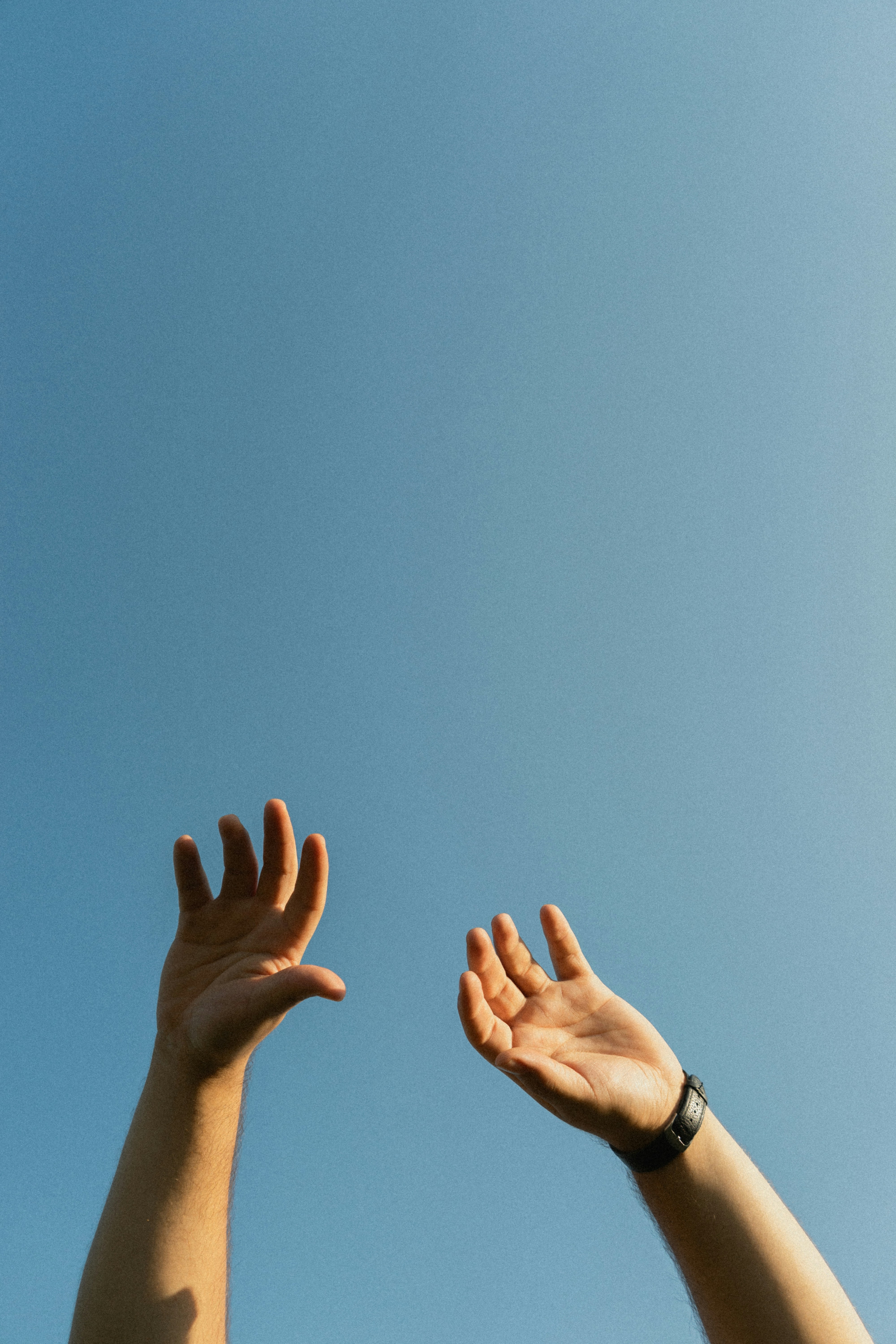 Two hands reaching upward against a clear blue sky, symbolizing aspiration and freedom.