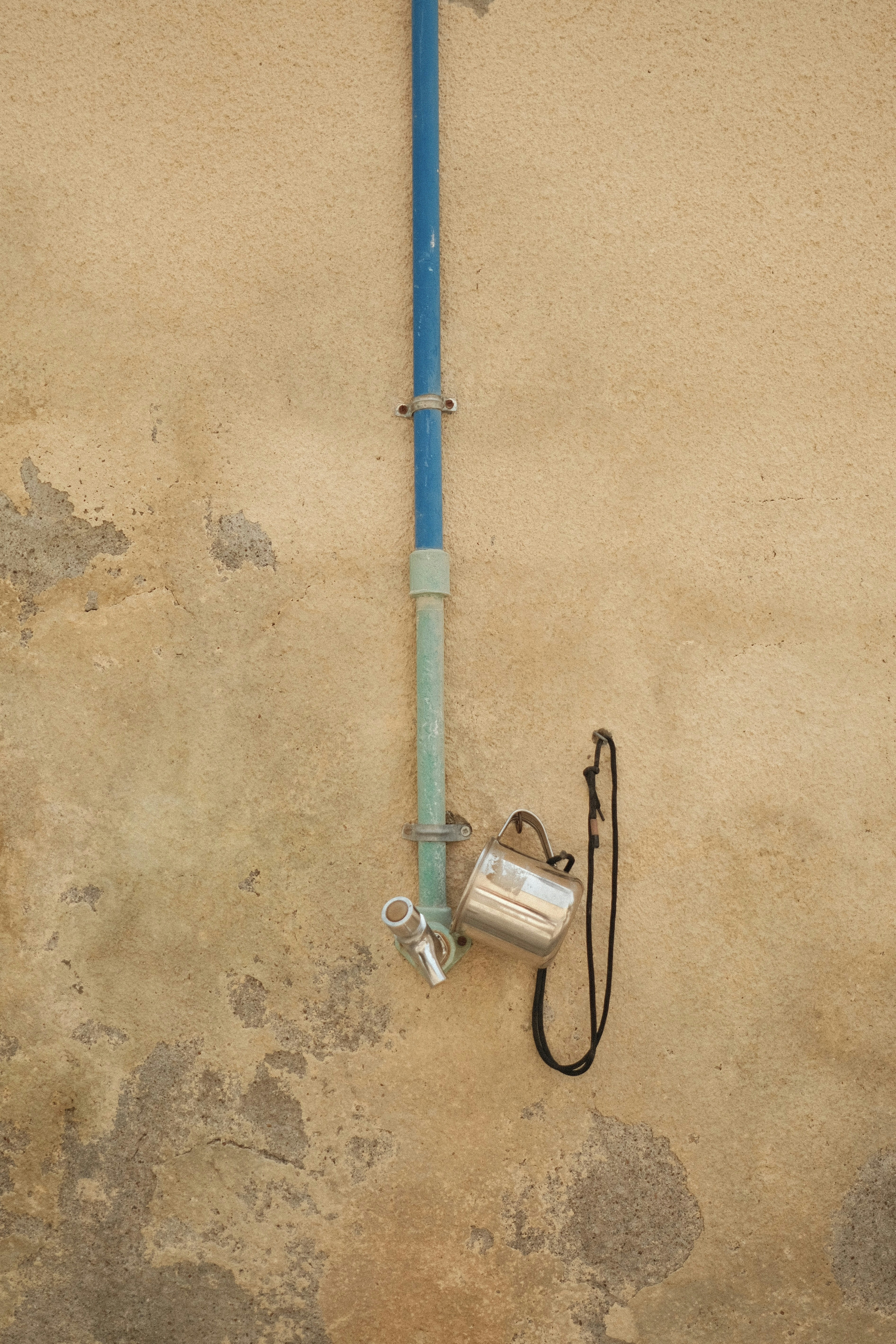 Blue Pipe Still Life: Wall-Hung Kettle on a Sunlit Facade