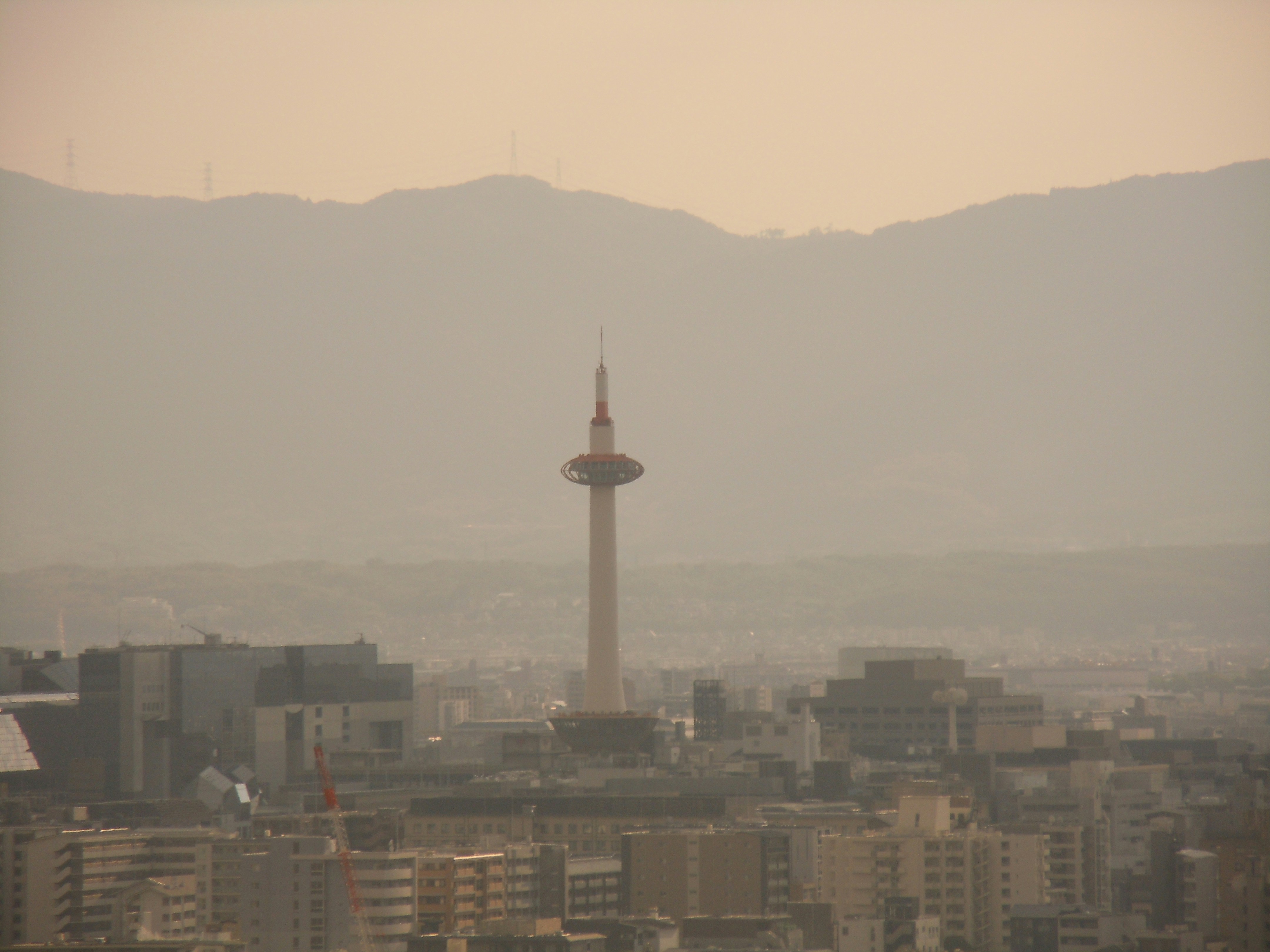 Kyoto Tower stands tall against a soft, hazy backdrop of mountains, capturing the essence of the city’s skyline.