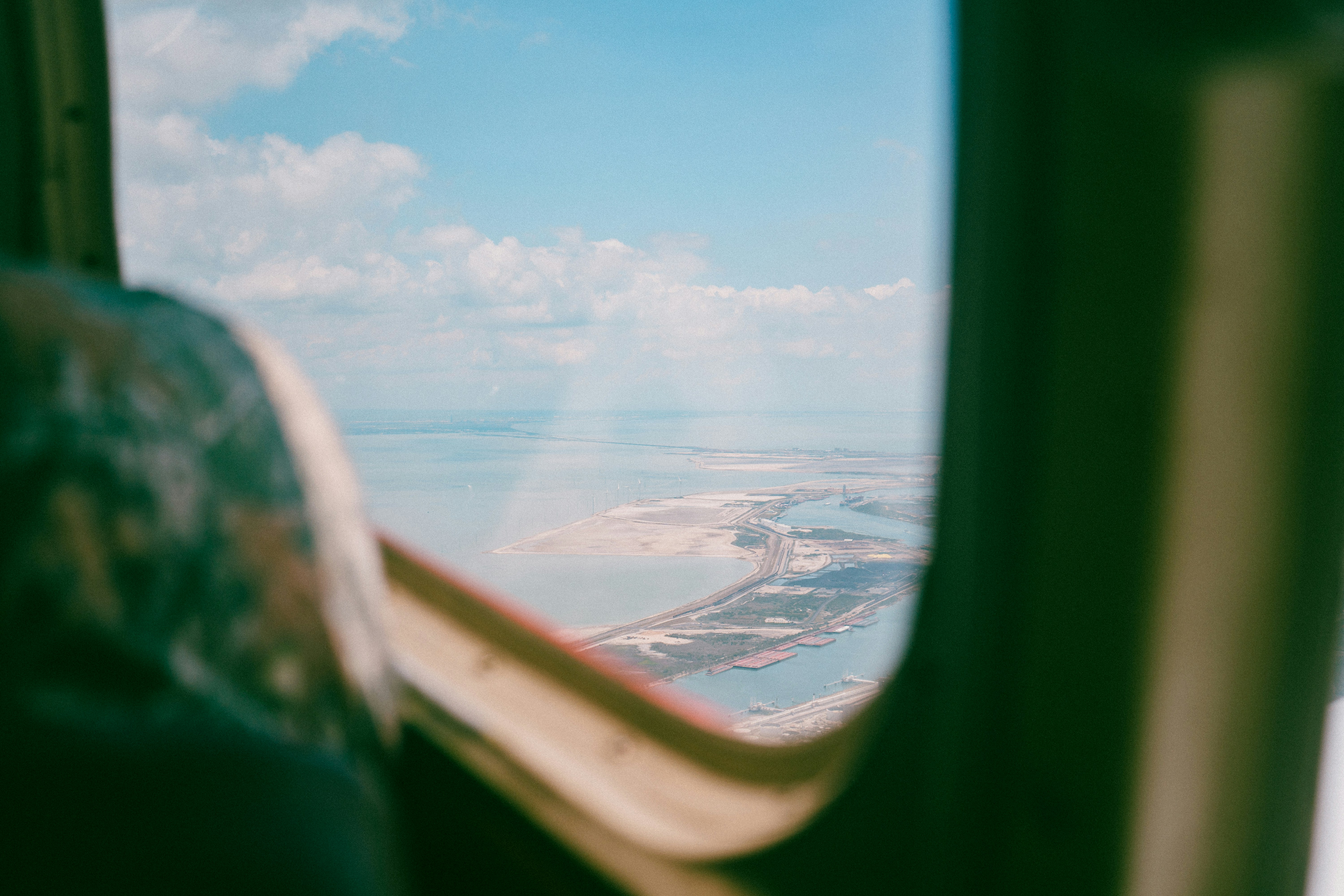 View from an airplane window showcasing a coastal landscape with water and land formations. The scene captures the interplay of colors and textures in nature.