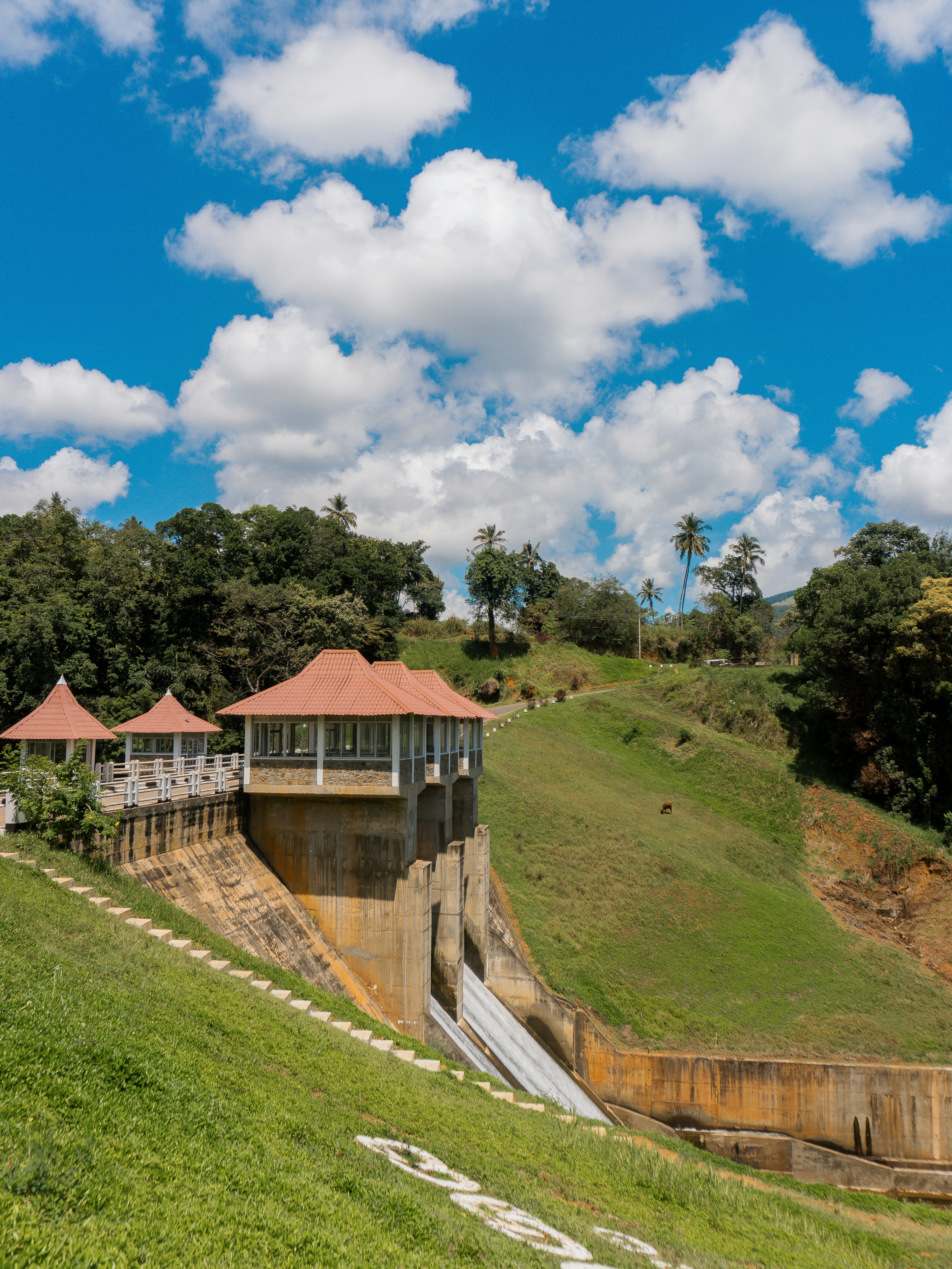 Terracotta-Roofed Pavilion Over a Hilltop Dam Beneath a Sky of Puffy Clouds