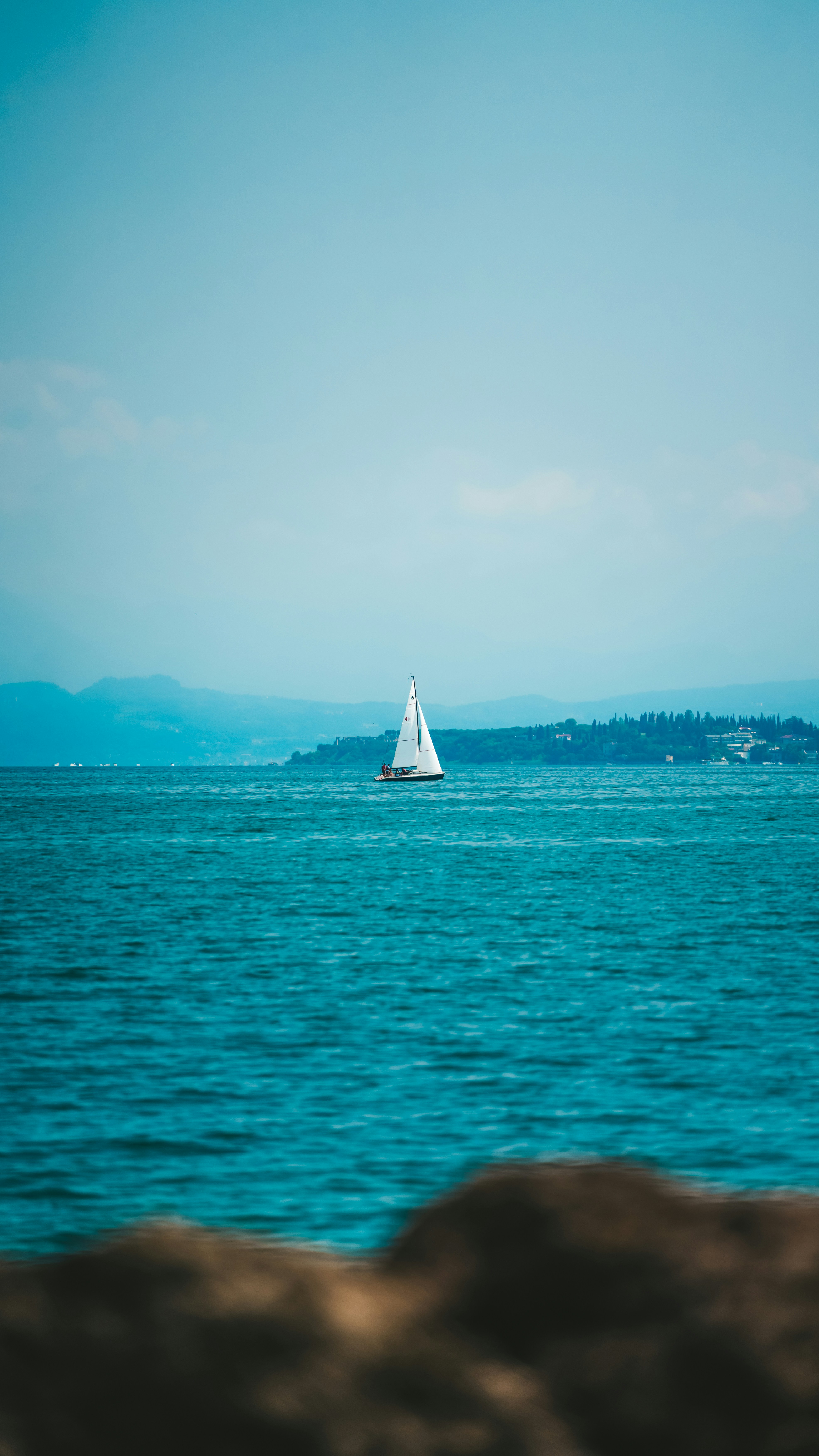 Sailboat gliding across a calm sea under a clear blue sky, with distant mountains framing the horizon.