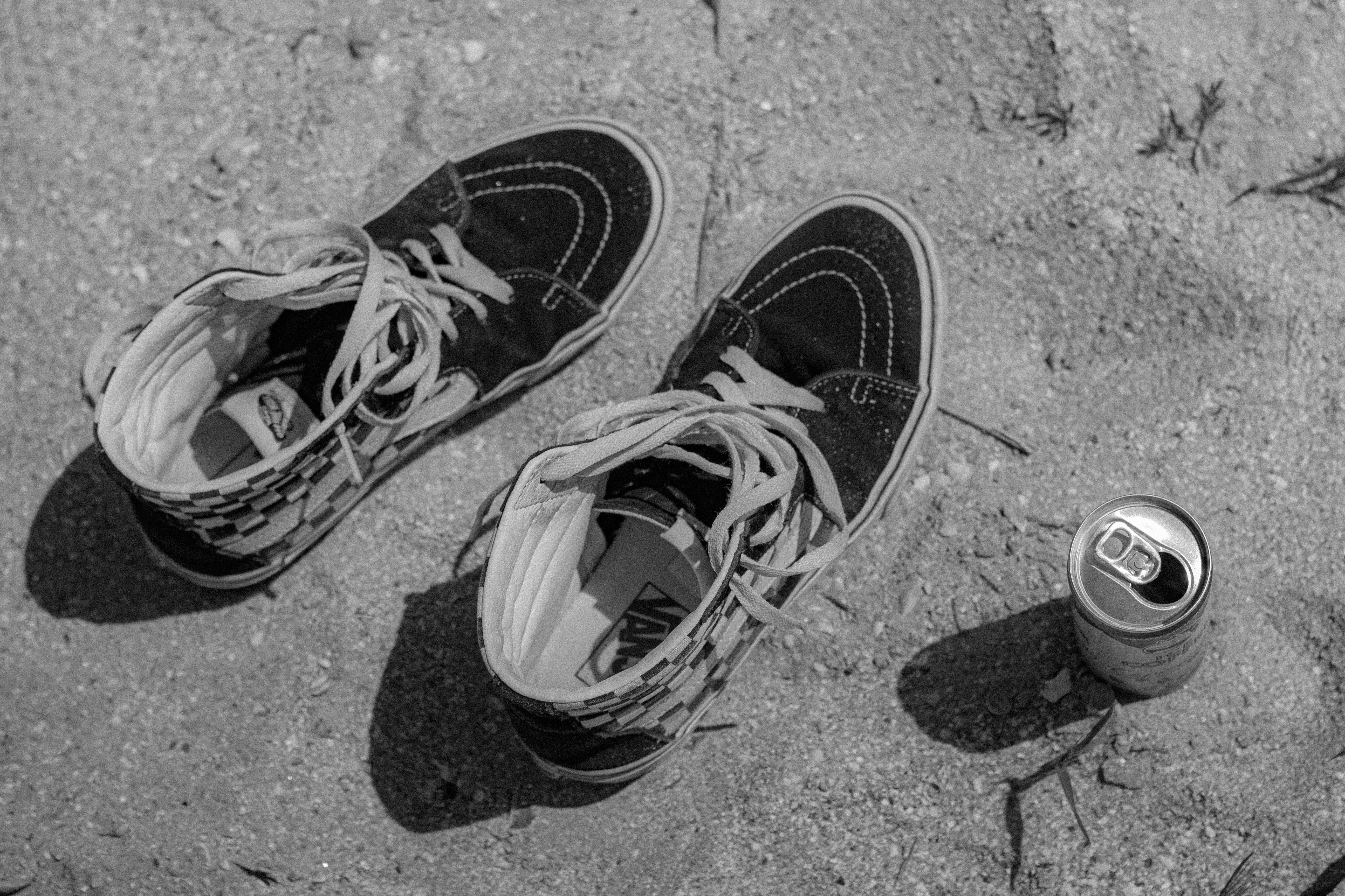Monochrome Pause: Sneakers Rest Beside a Soda Can on Parched Ground