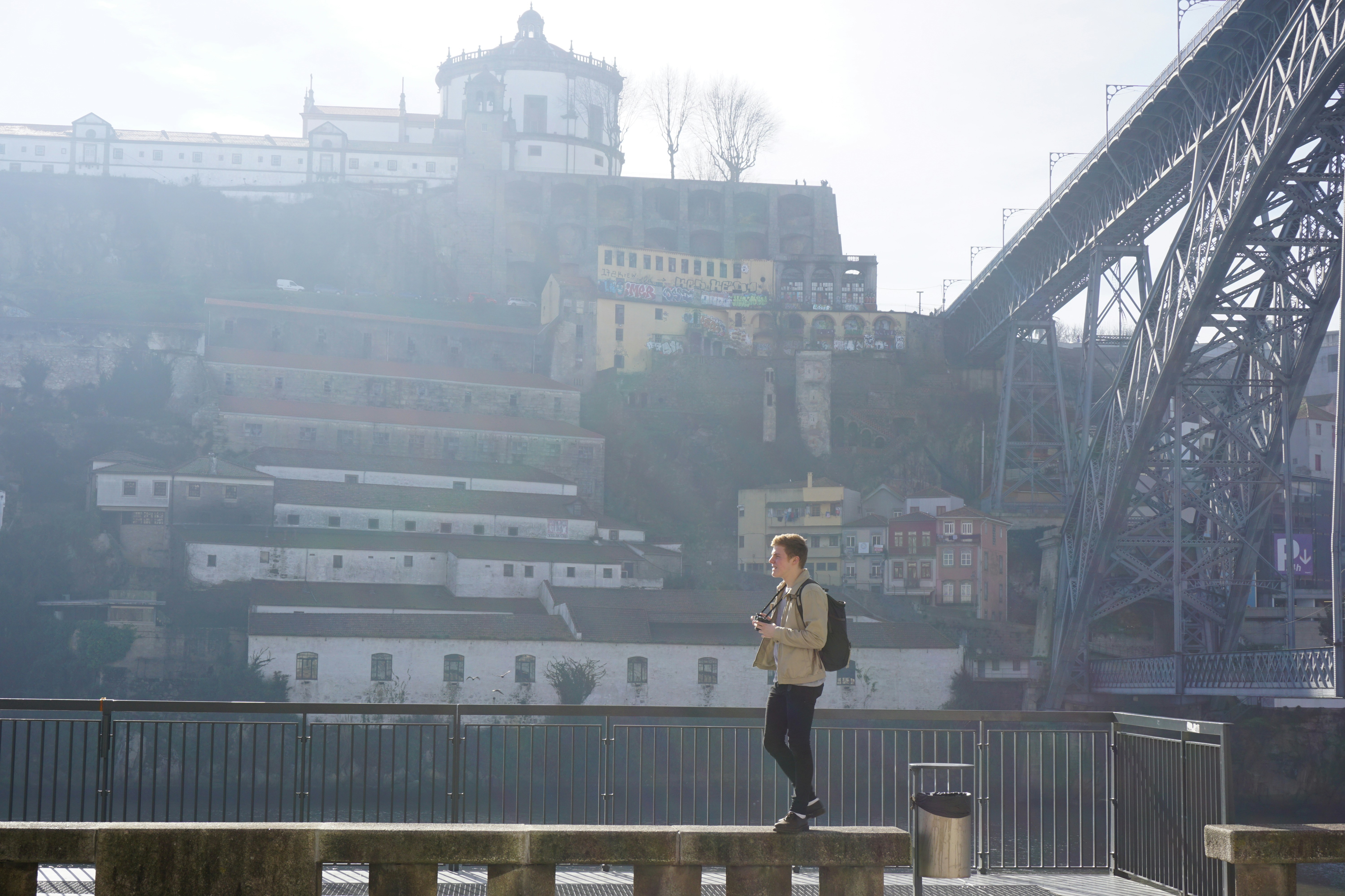 Mist-Clad Riverside Pause: A lone traveler beneath Porto's Dom Luís I Bridge