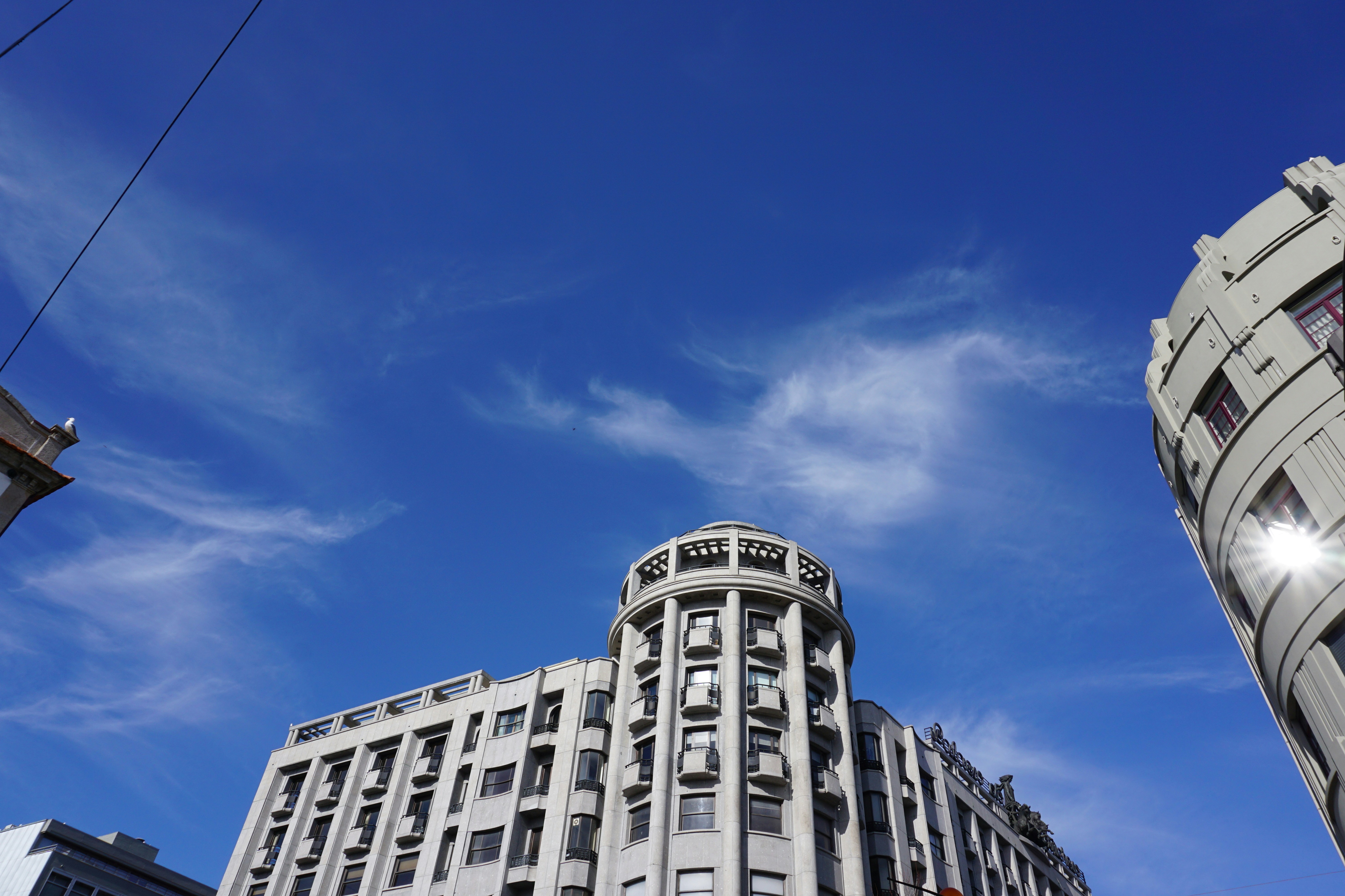 A historic building's rounded facade rises against a clear blue sky, showcasing intricate architectural details and soft cloud patterns.