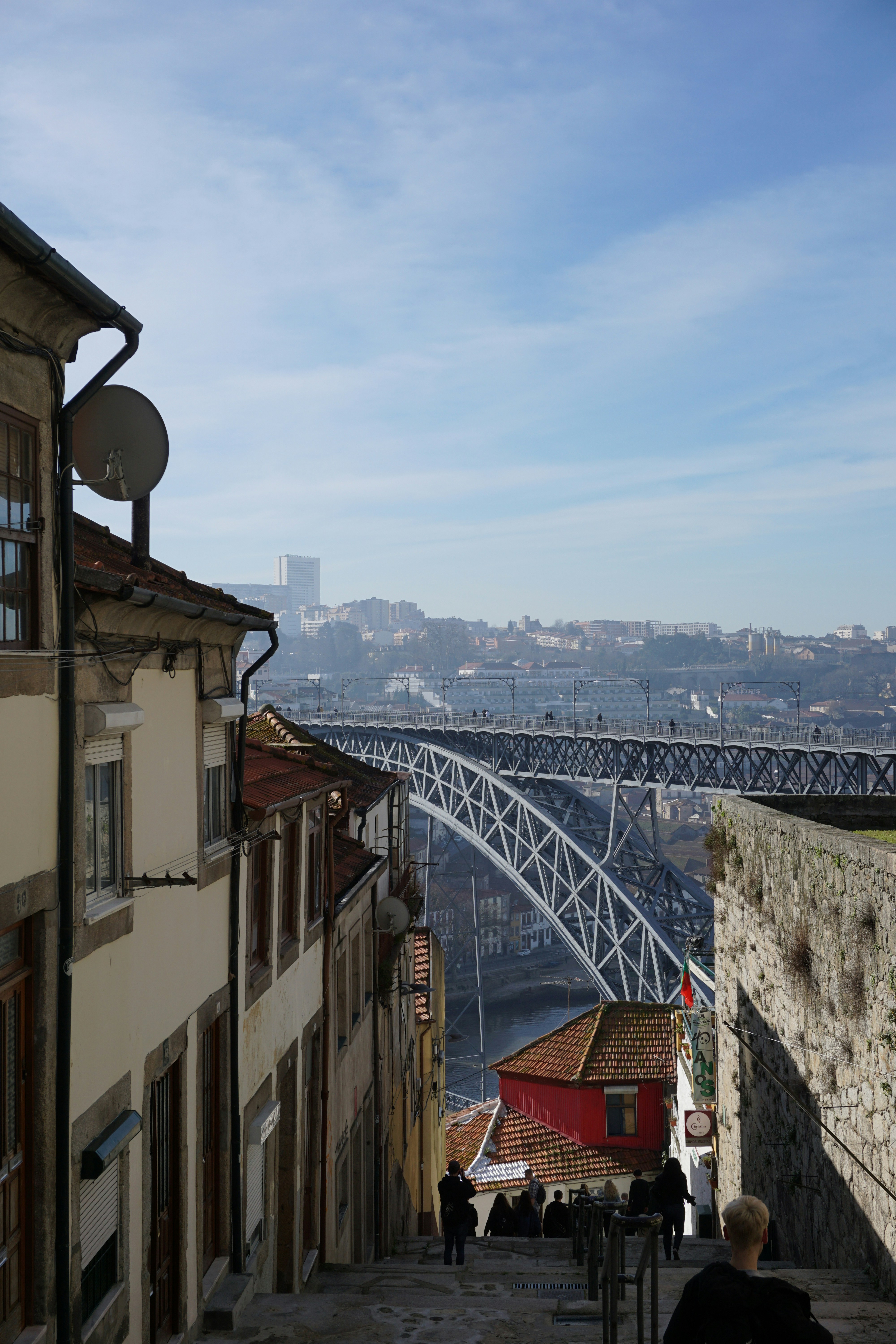 Narrow cobblestone street leading down to the iconic Dom Luís I Bridge, with quaint buildings lining the path and a glimpse of the cityscape in the background.