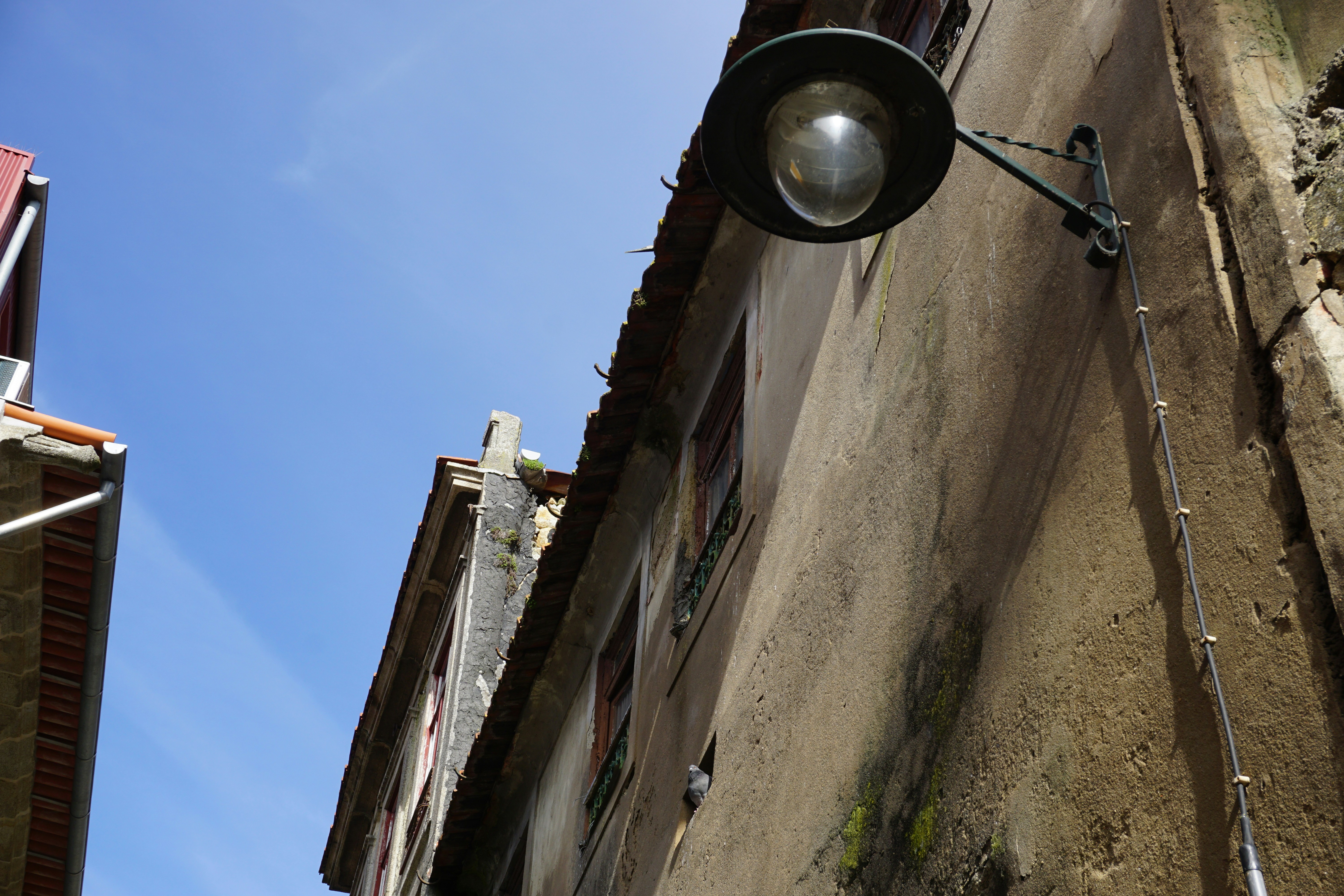 A vintage street lamp casts light on a textured wall of an old building, showcasing the contrast between urban elements and weathered architecture.