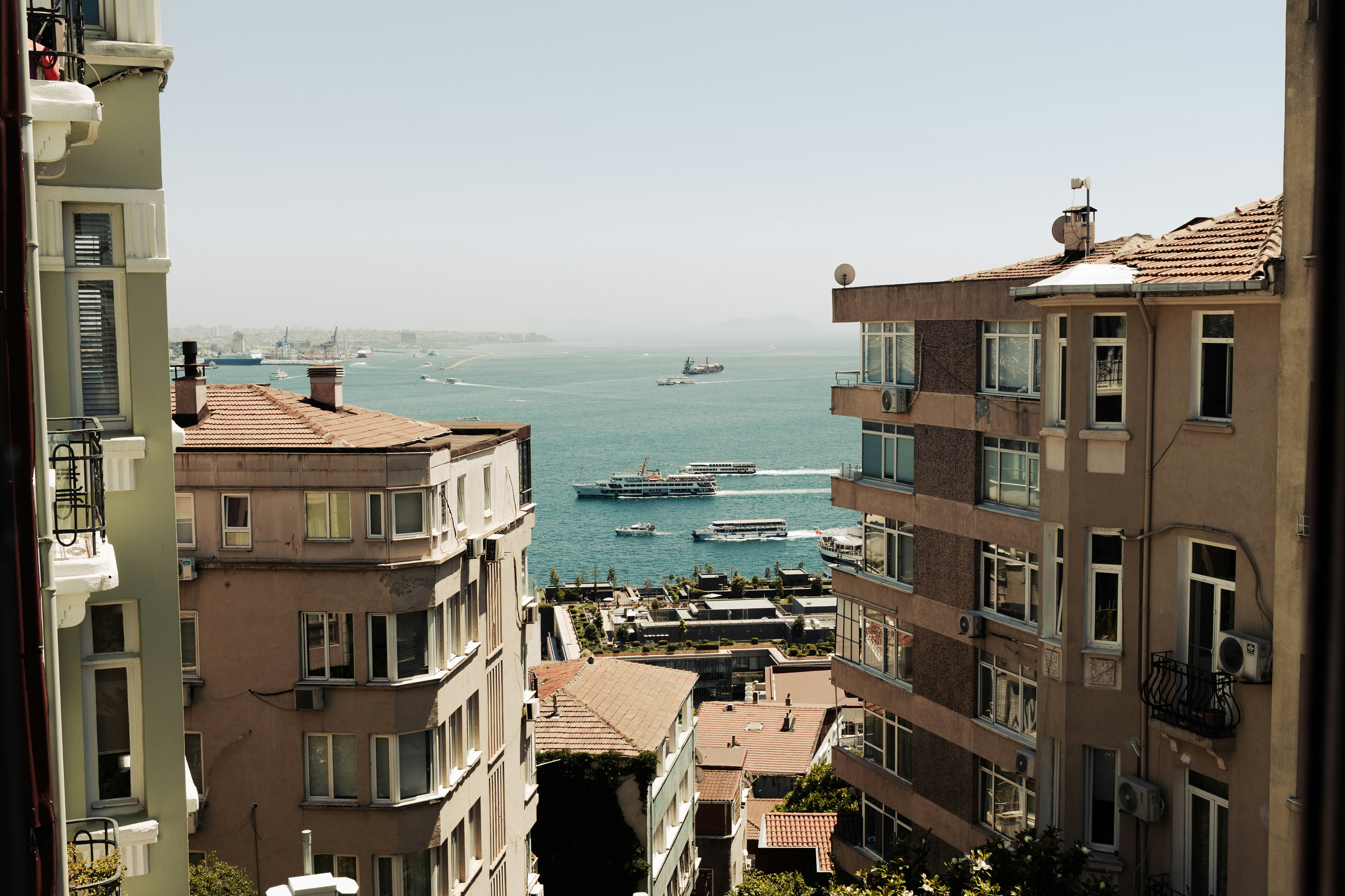 A panoramic view of the Bosphorus Strait framed by residential buildings, showcasing boats navigating the serene waters. The scene captures a blend of urban life and natural beauty.