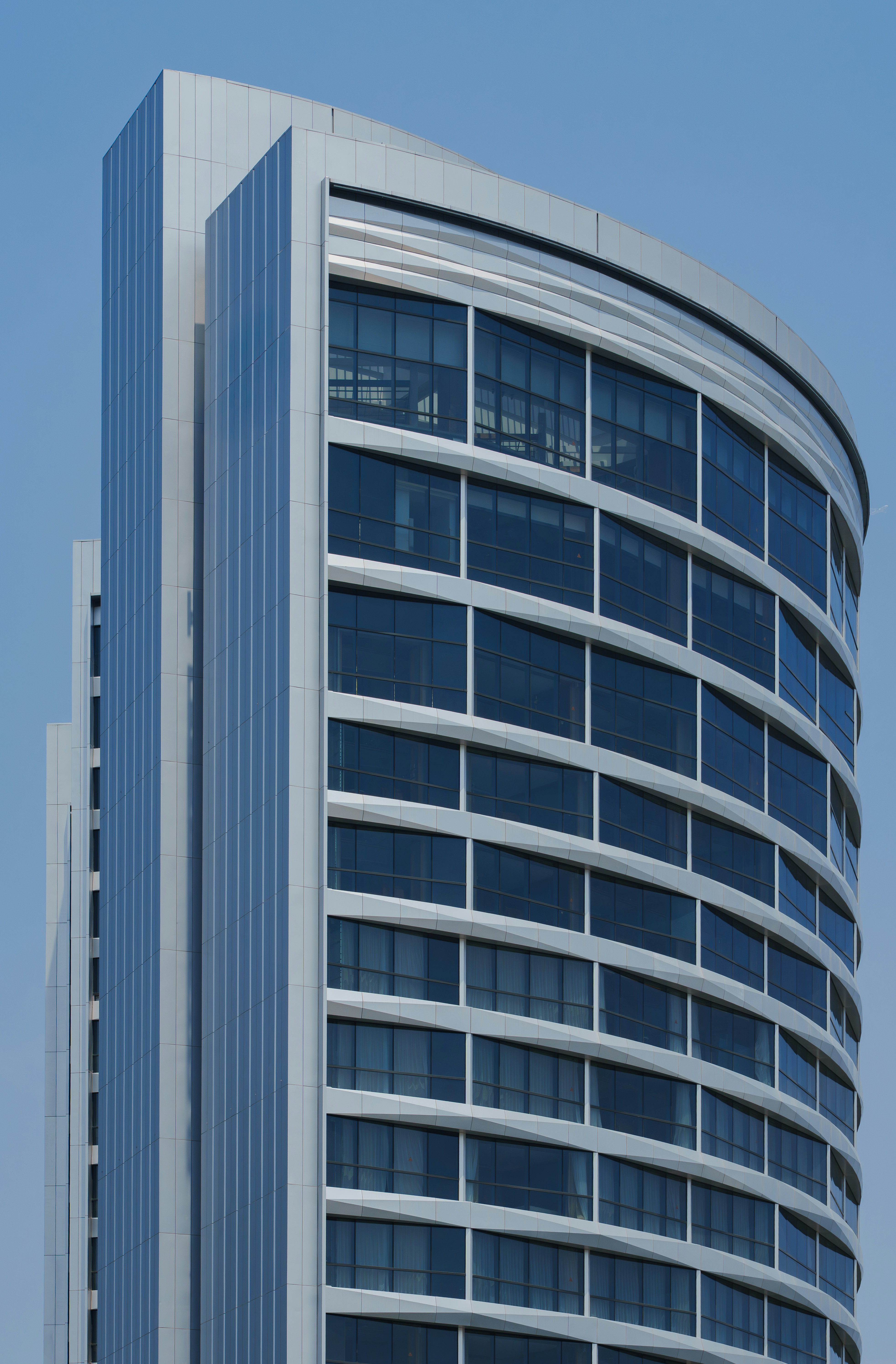 Sleek curved building facade showcasing reflective glass and metallic elements against a clear blue sky.