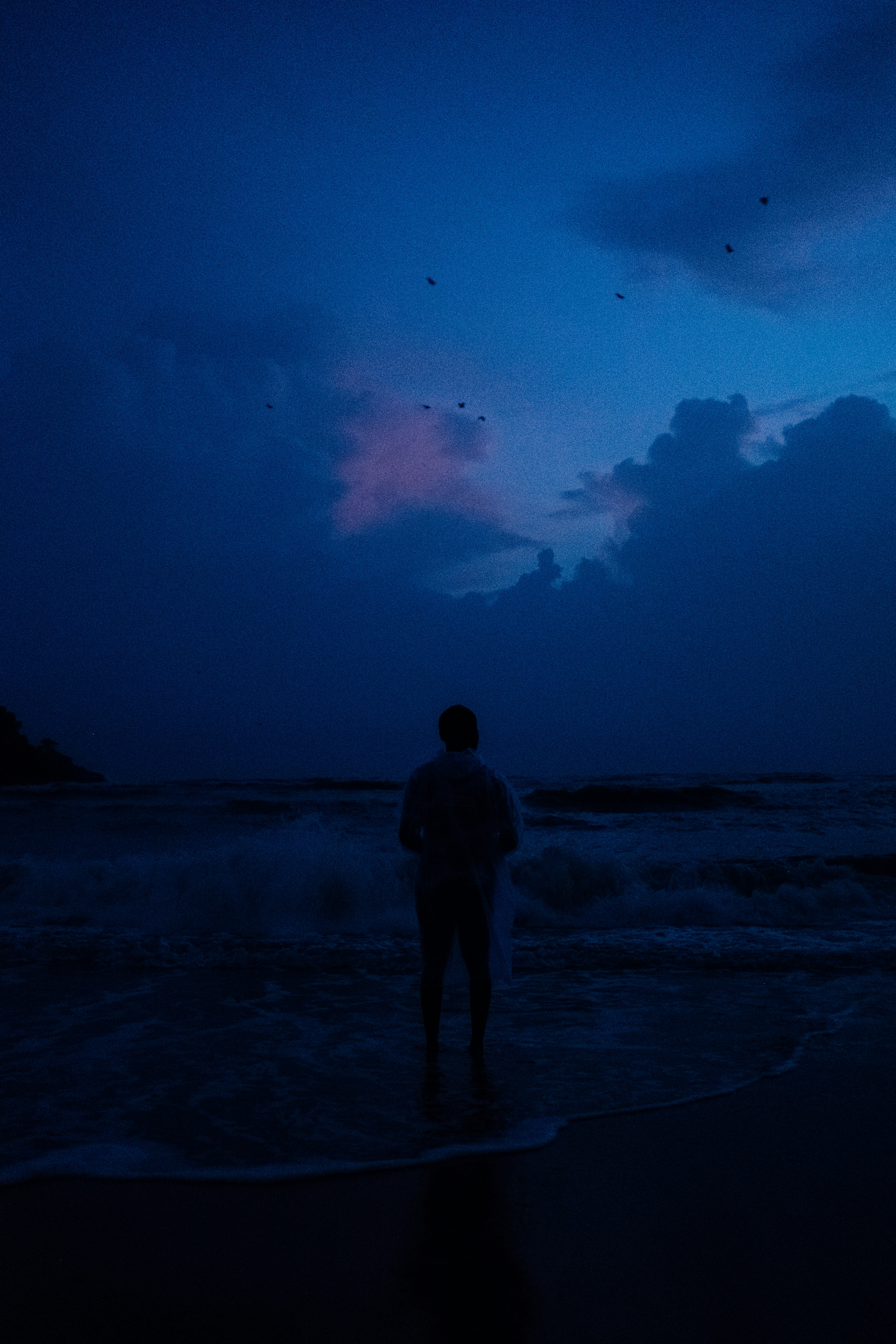In heart of the heart of the monsoon | A person stares out at the ocean at night.