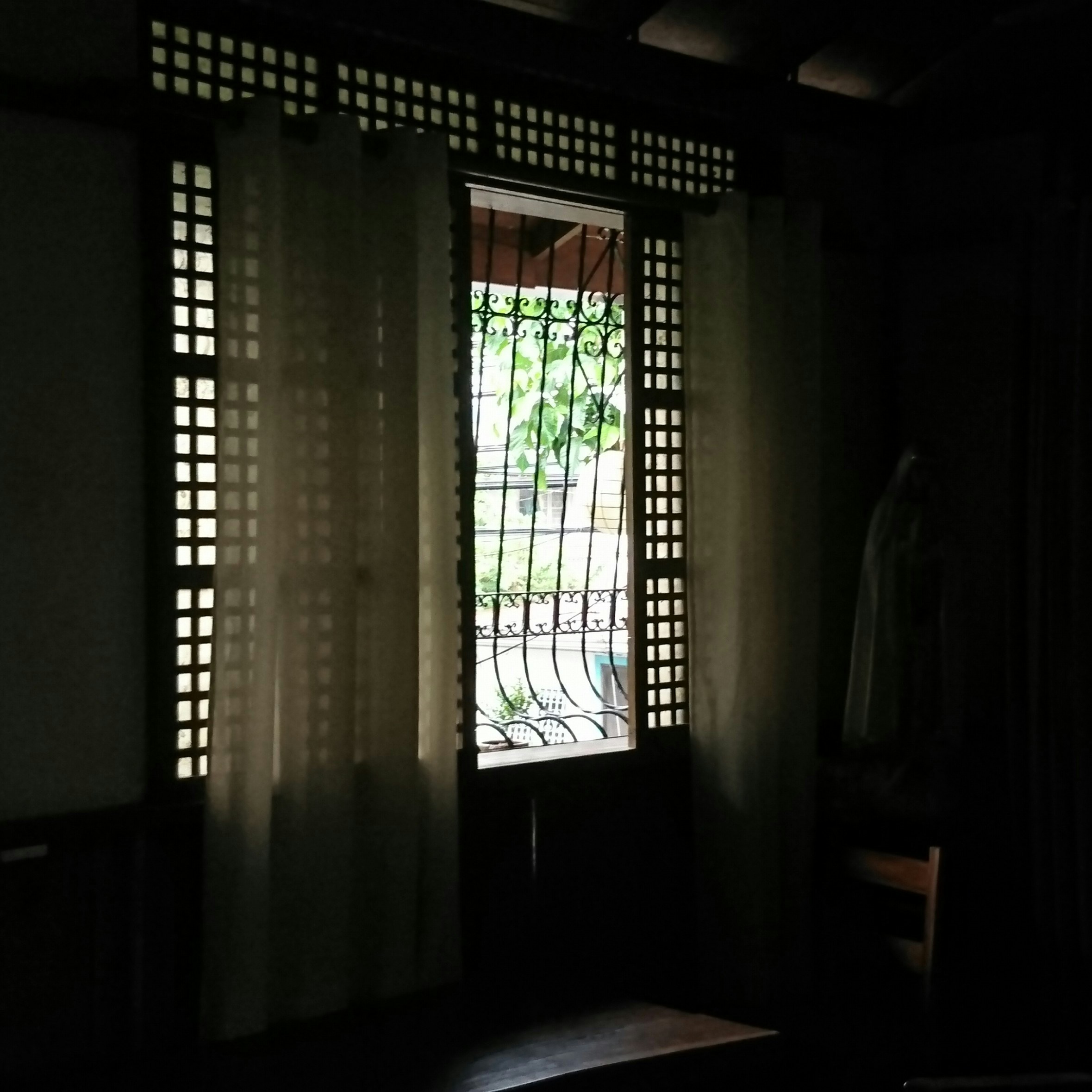 Softly lit interior with sheer curtains framing a window, allowing glimpses of greenery outside. The interplay of light and shadow creates a tranquil atmosphere.