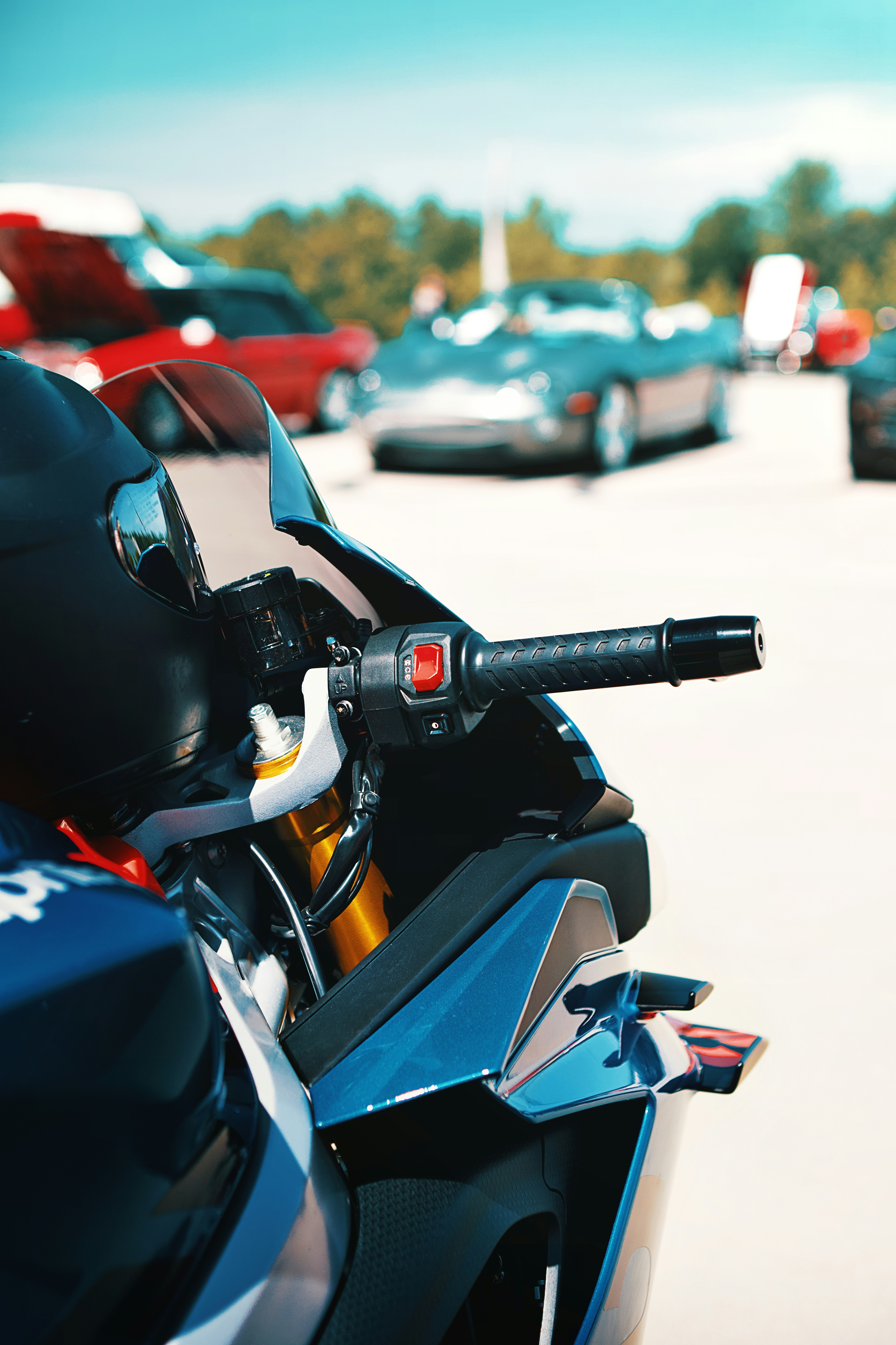 Close-up of a motorcycle's handlebar and controls, showcasing intricate details and craftsmanship. The background features blurred cars, emphasizing the bike's design.