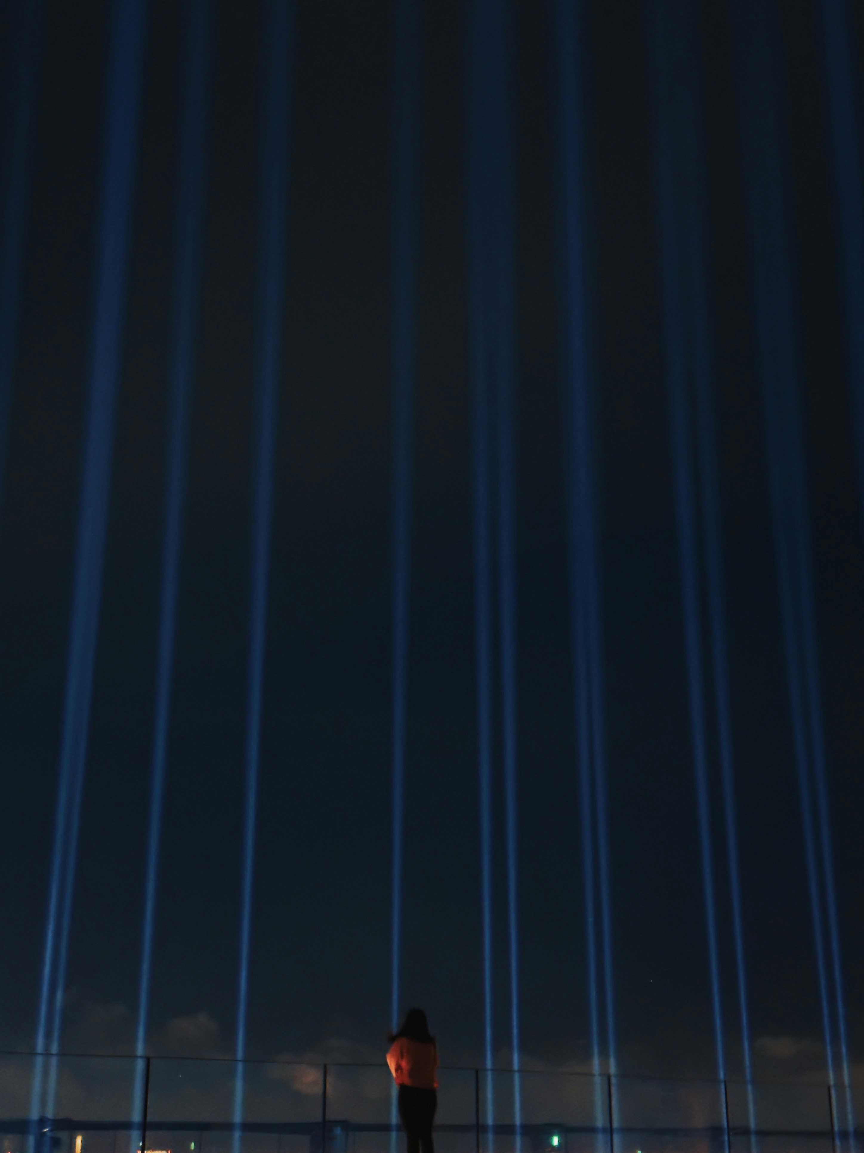 Person watches illuminated light beams in the night.
