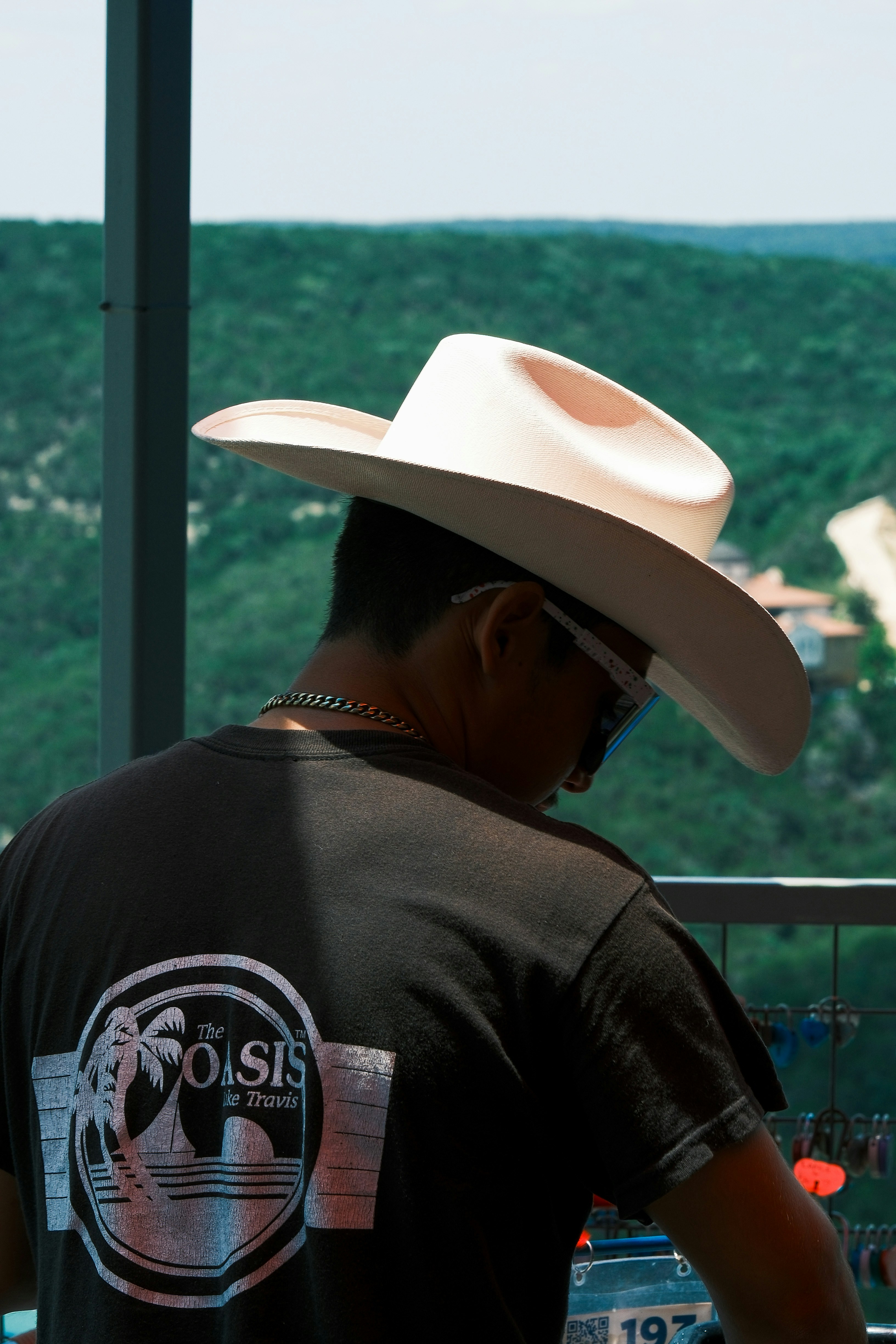 A man in a cowboy hat looking down from a scenic viewpoint at The Oasis on Lake Travis. An intimate moment under the Texas sun.