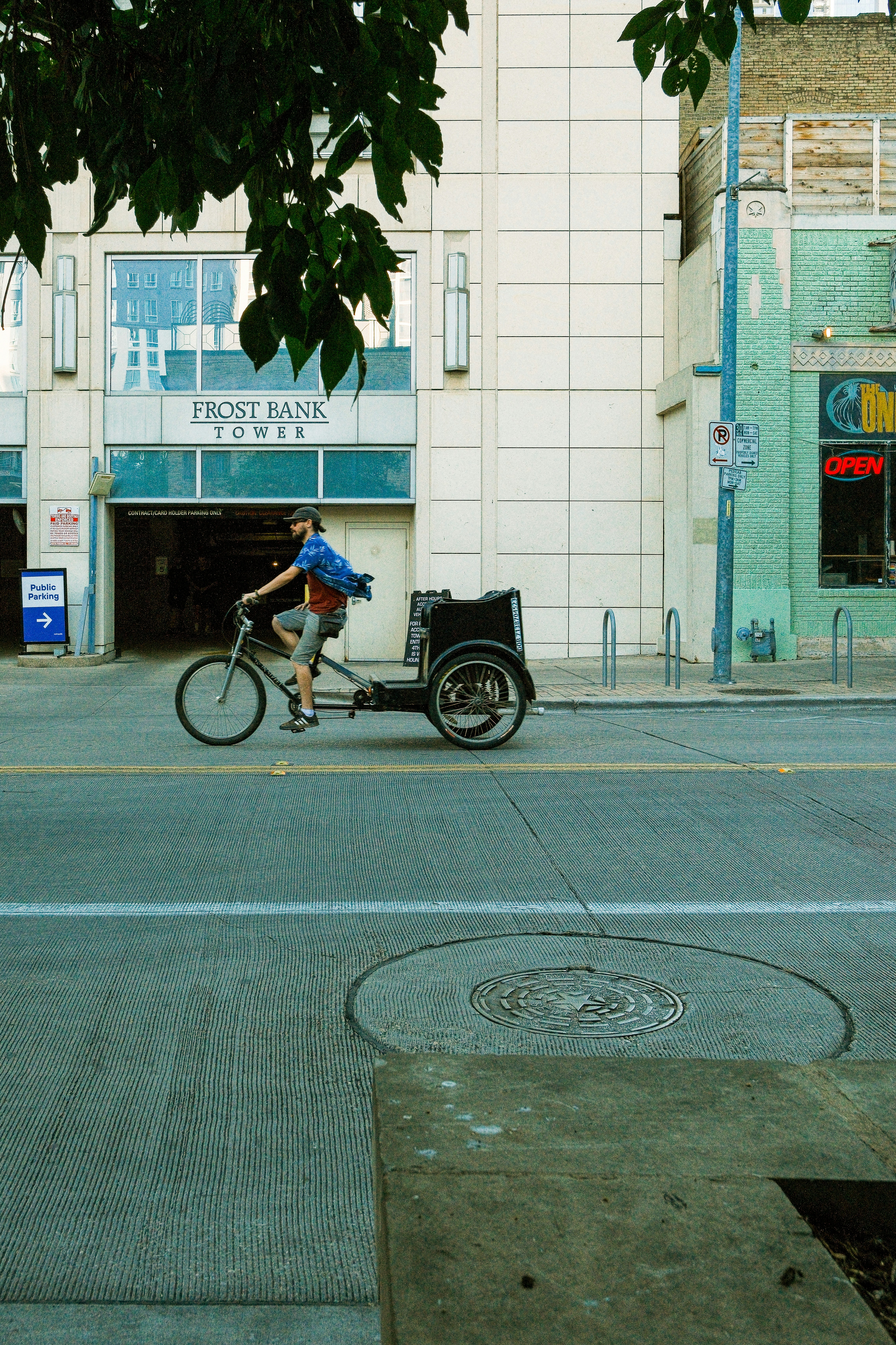 A street pedicab driver rides past the Frost Bank Tower in Austin, captured mid-motion with urban textures in the backdrop. | A pedicab rides down the street.