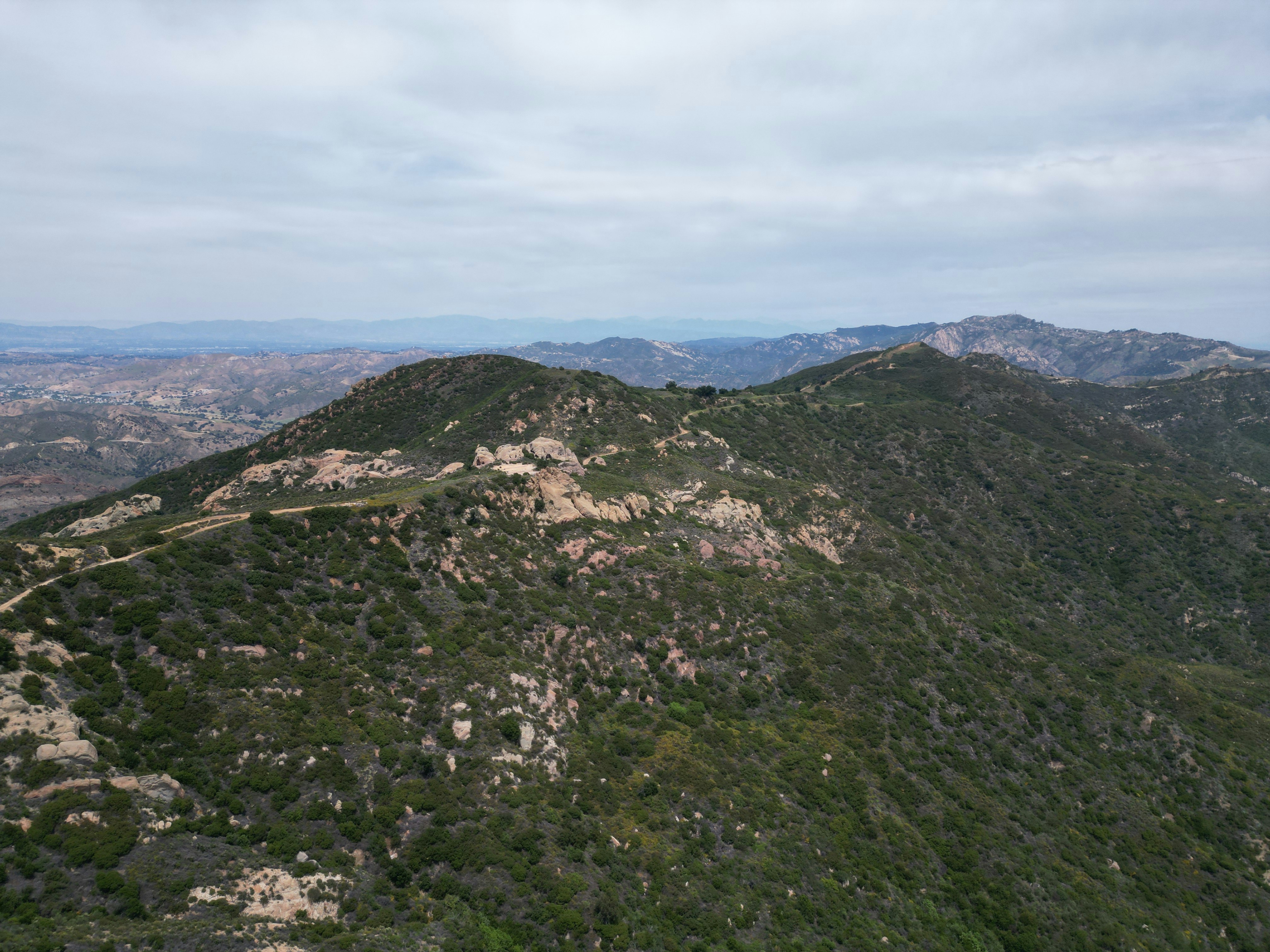 Aerial view of rolling hills and winding paths, showcasing the lush greenery and rocky outcrops of the landscape. The scene captures the serene beauty of nature's contours.