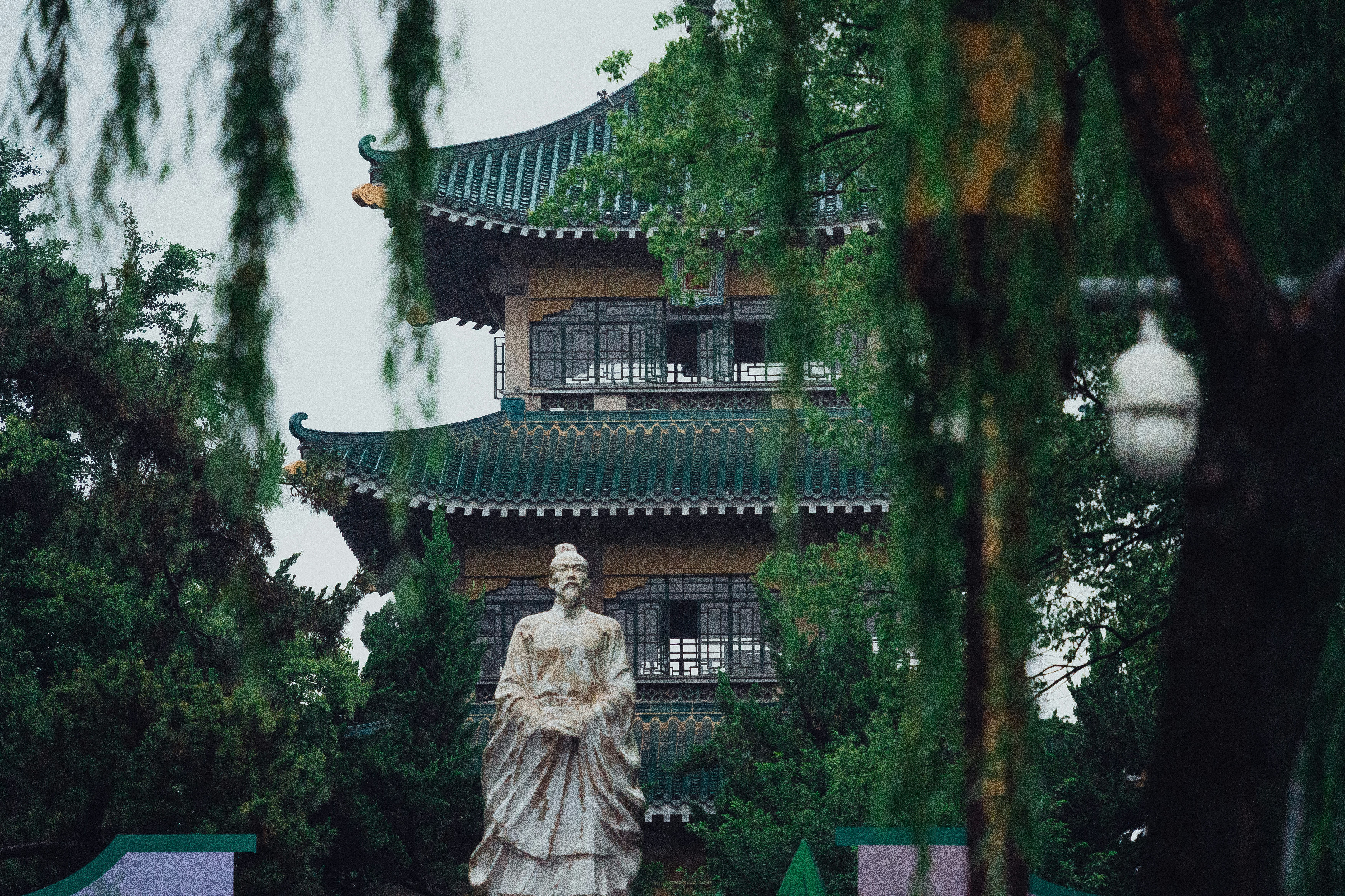 Elegant statue in foreground with traditional pagoda in background, surrounded by lush greenery.