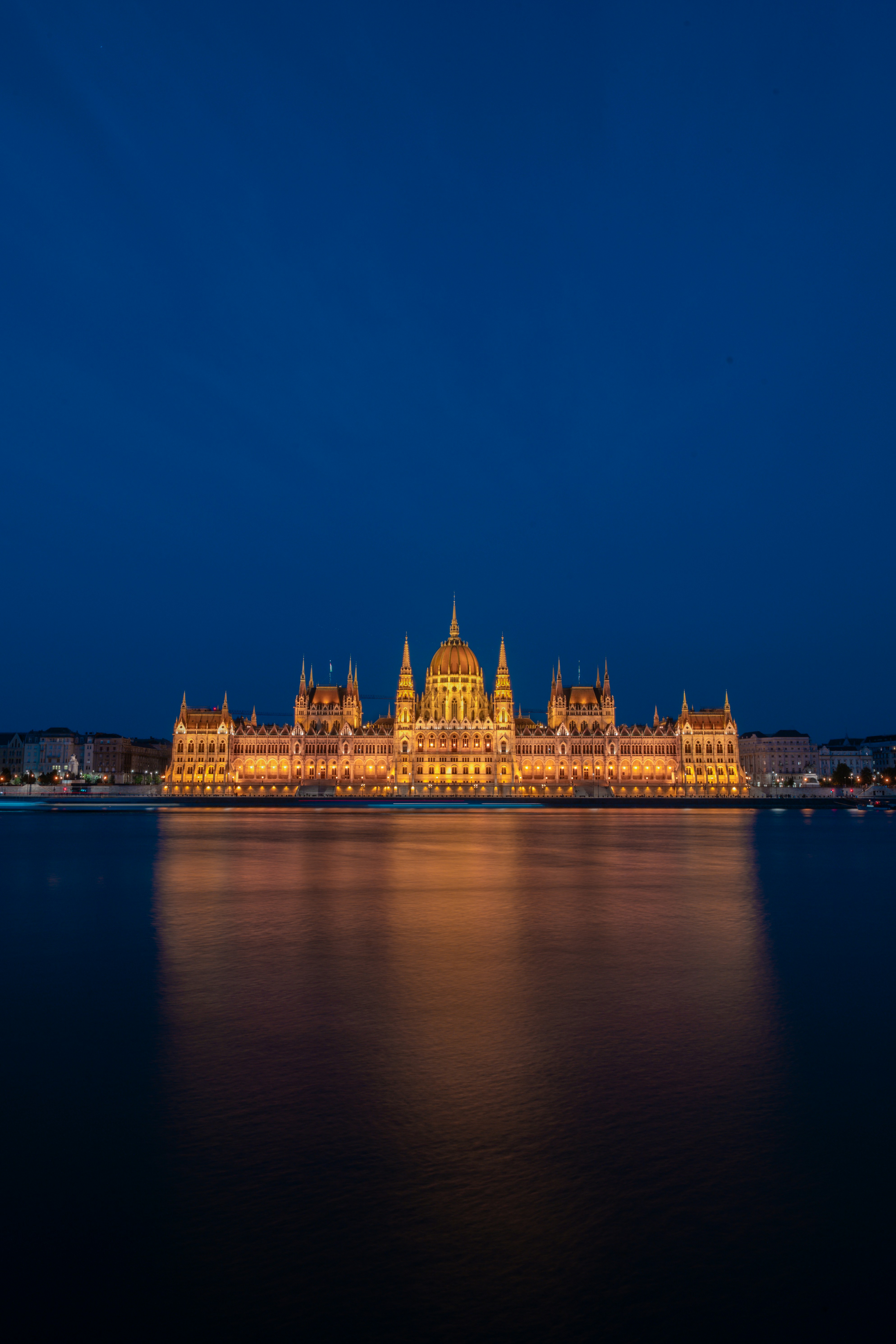Illuminated Hungarian Parliament Building reflecting on the Danube River during twilight.