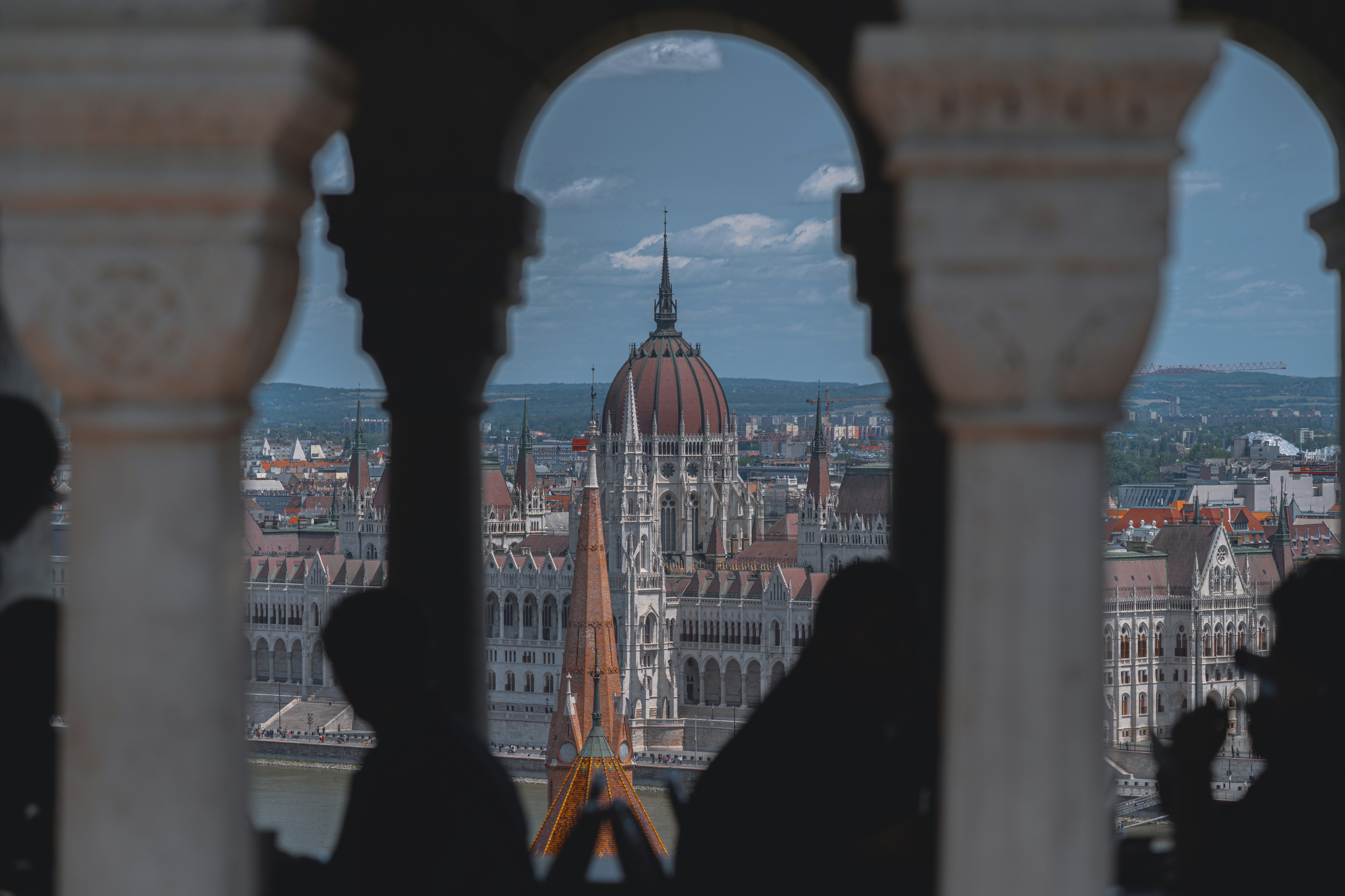 Silhouetted figures frame the iconic Hungarian Parliament building, showcasing its intricate architecture against a clear blue sky.
