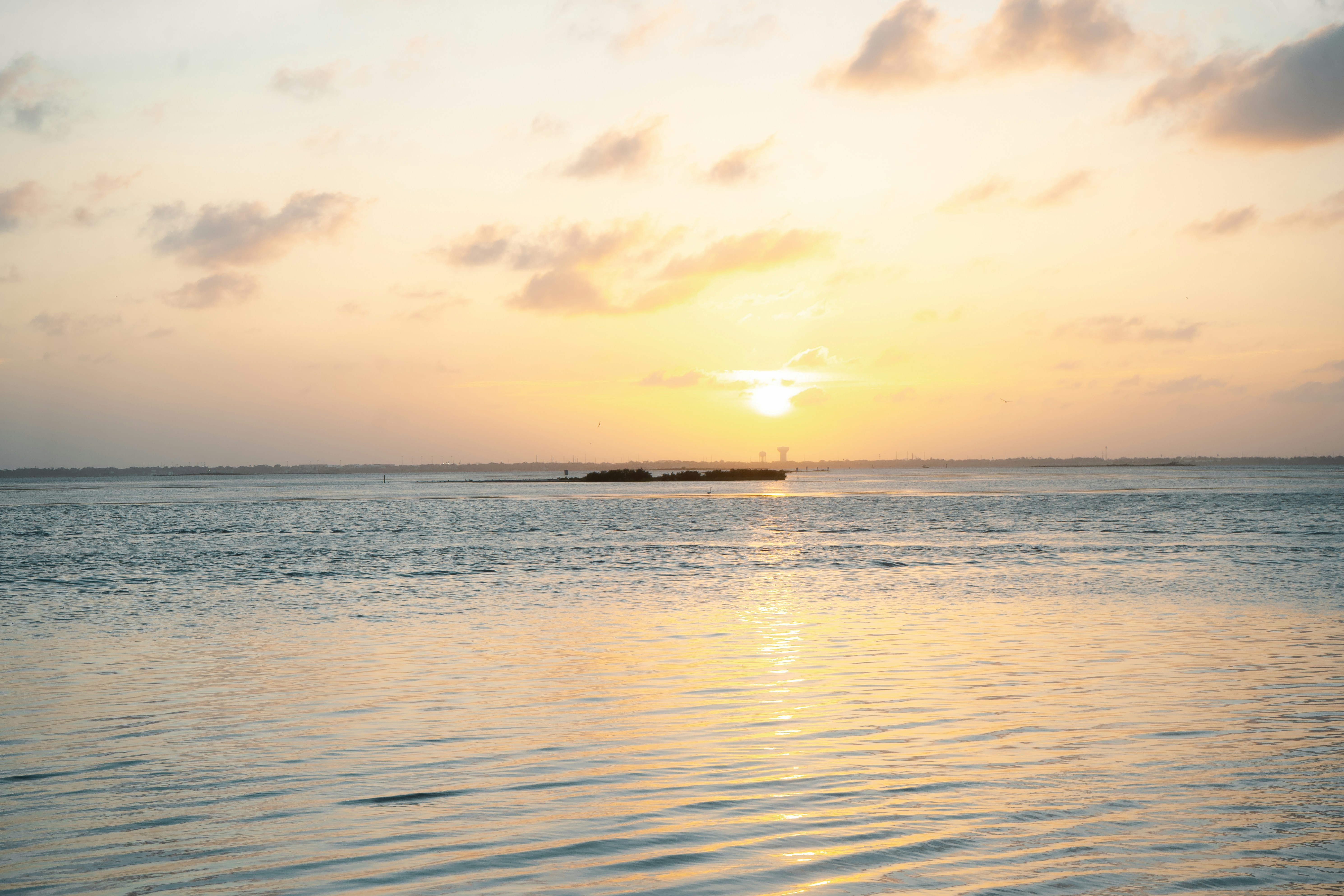 Golden sunset reflecting on tranquil waters, with a distant silhouette of land on the horizon.