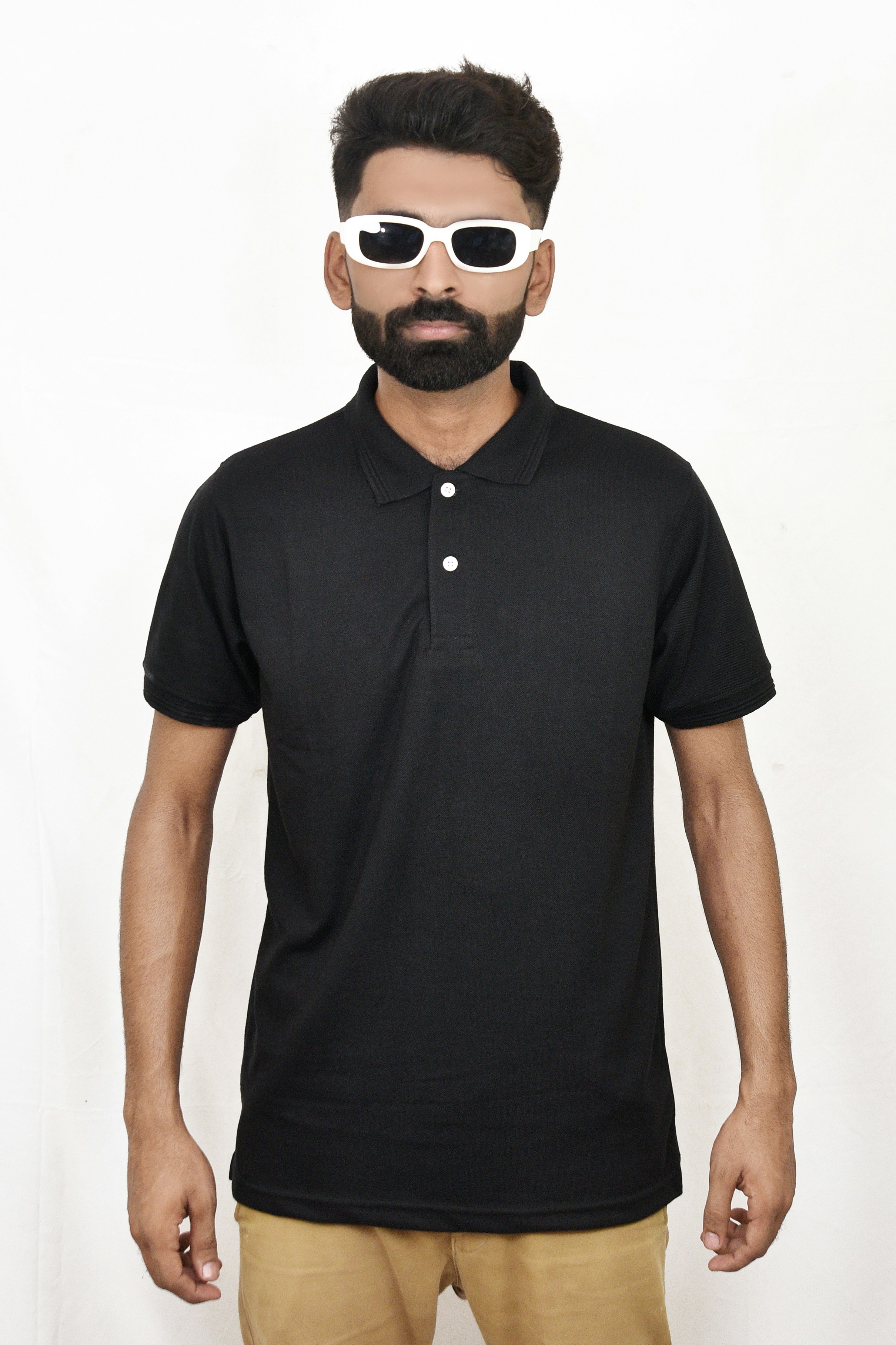 Individual in a black polo shirt and white sunglasses poses against a plain backdrop, exuding a contemporary fashion vibe.