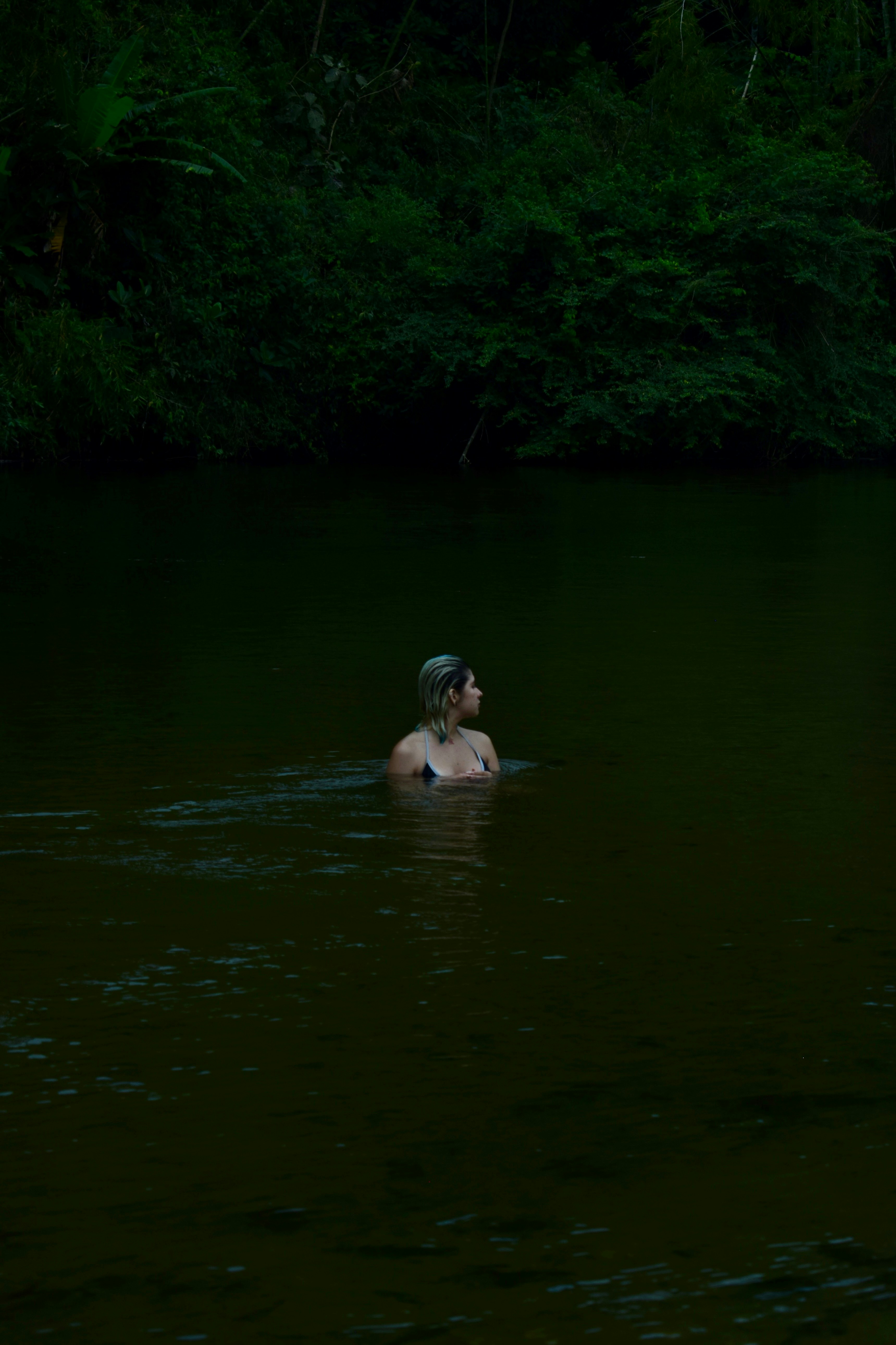 A woman wades through a serene river, surrounded by lush greenery, embodying tranquility and connection with nature.