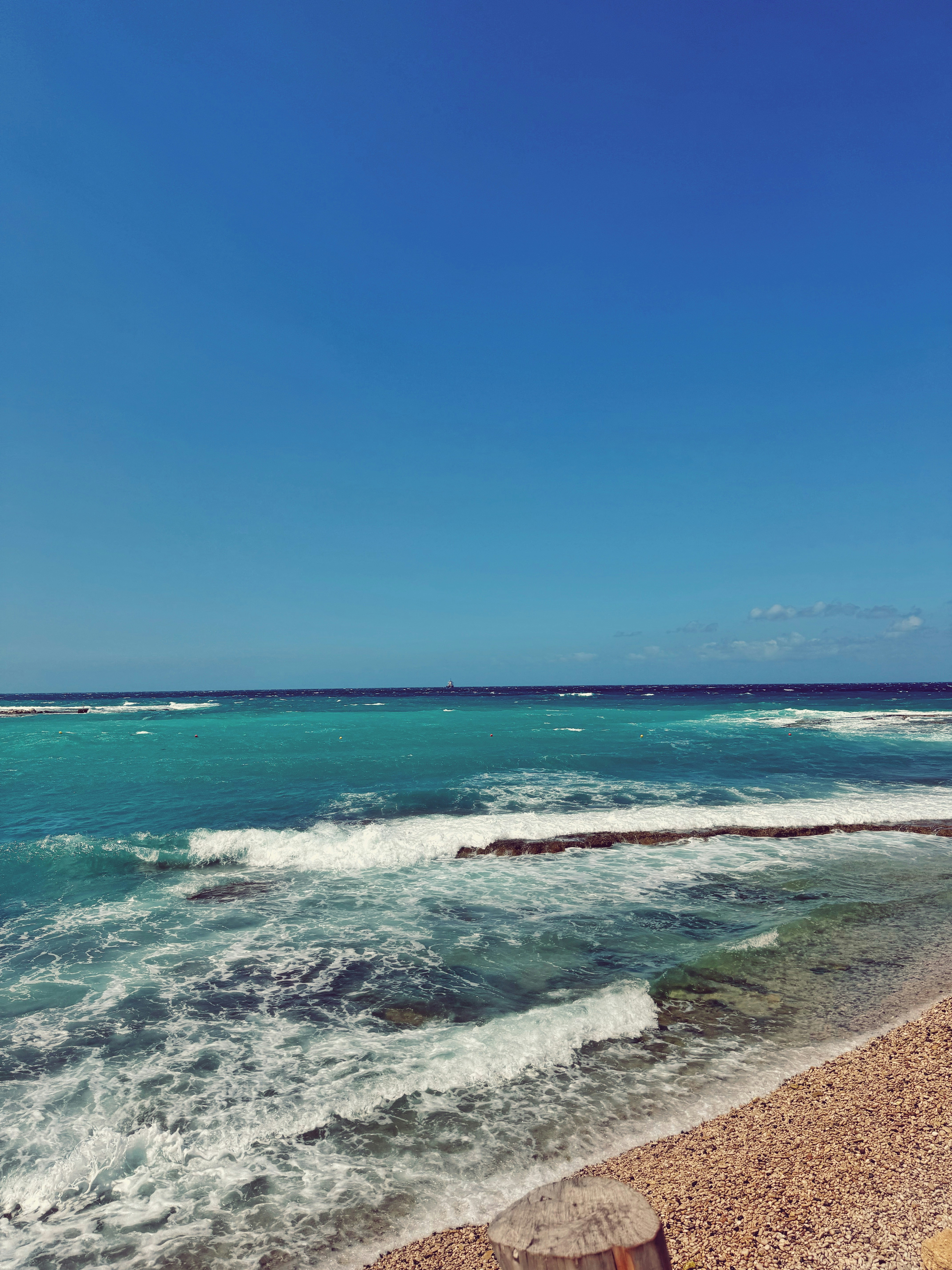 Gentle waves lapping against a pebbled shore under a clear blue sky, evoking tranquility and connection with nature.