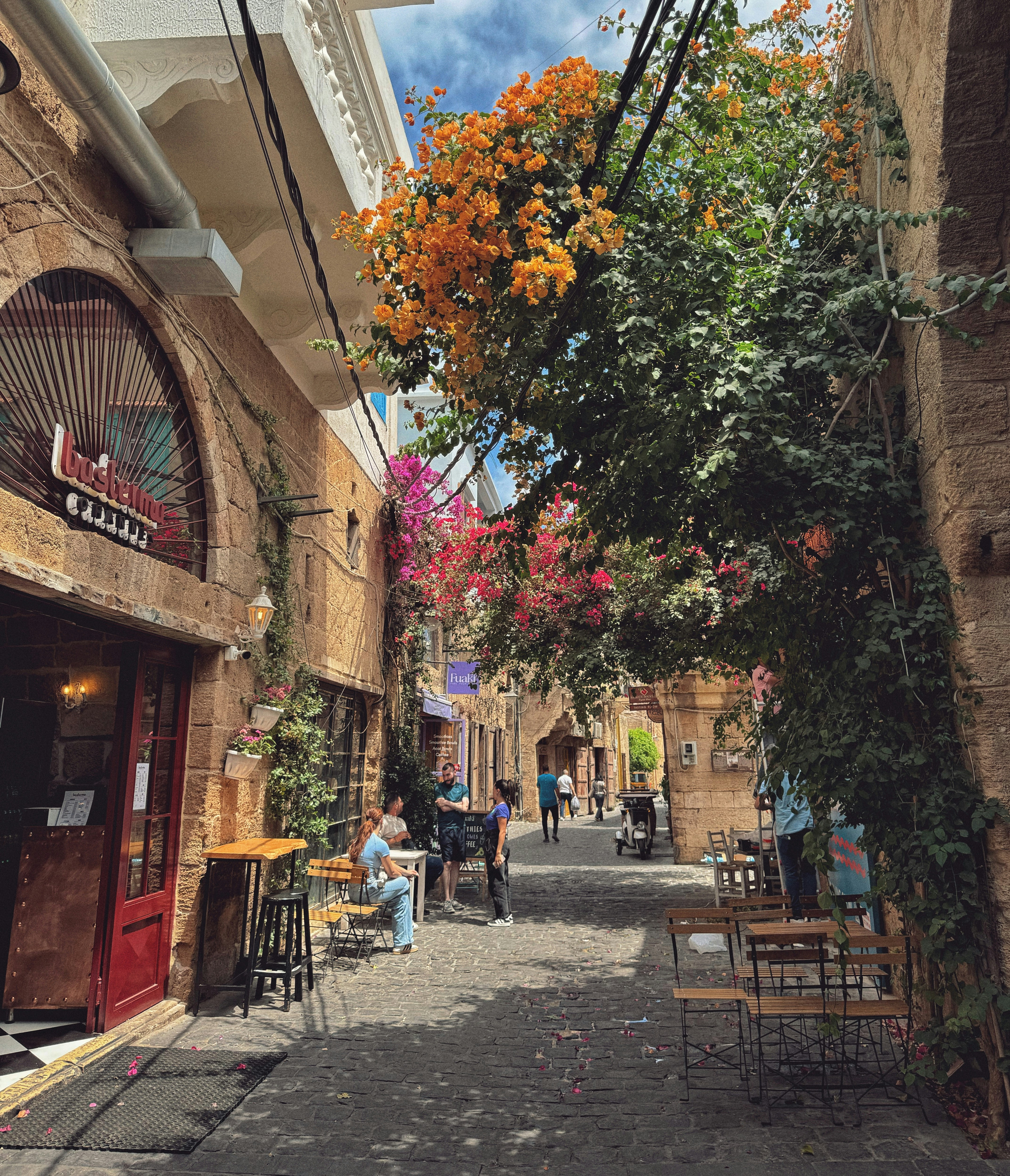 Cobbled Alley Café in Bloom: Sunlit Seating Beneath Cascades of Orange and Pink