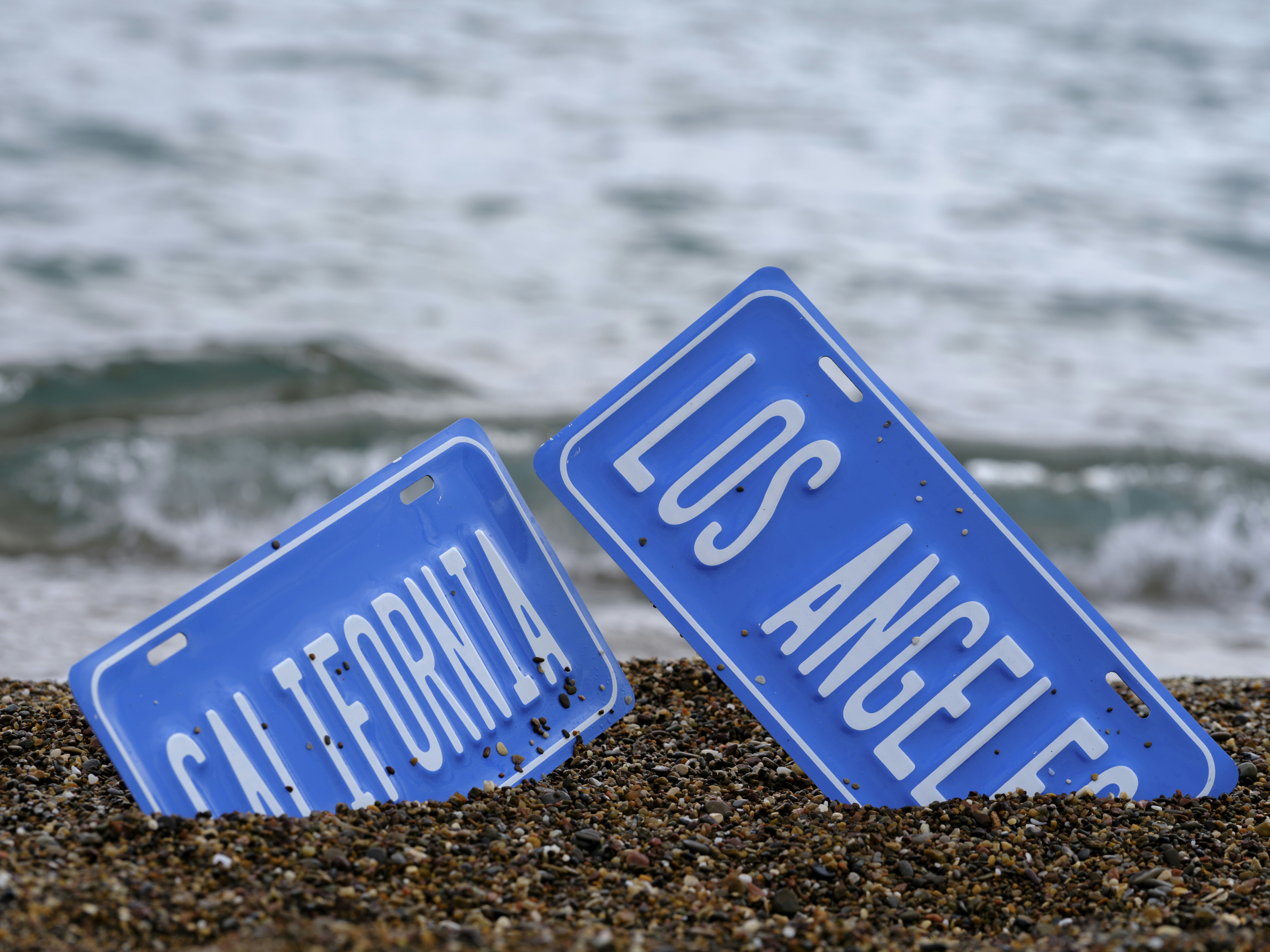 Blue Street Sign Duo Sunk in Pebbled Shoreline