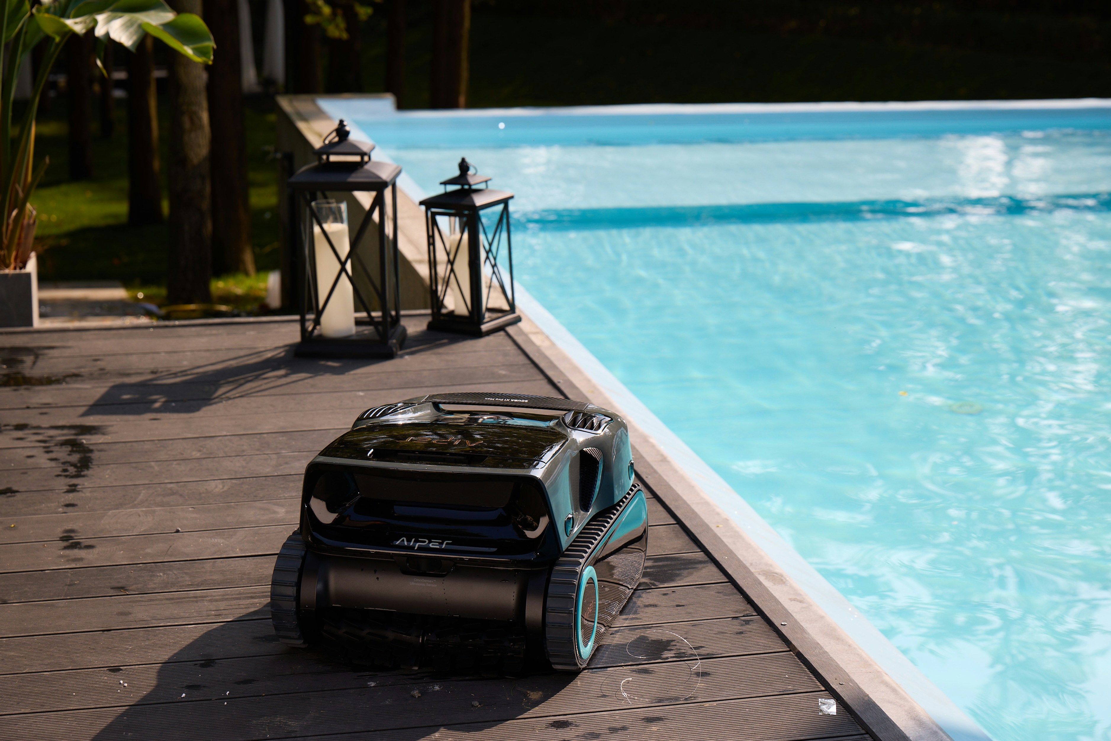 A robotic pool cleaner resting on a wooden deck beside a shimmering blue pool, accentuated by stylish lanterns. The scene embodies modern convenience in outdoor living.