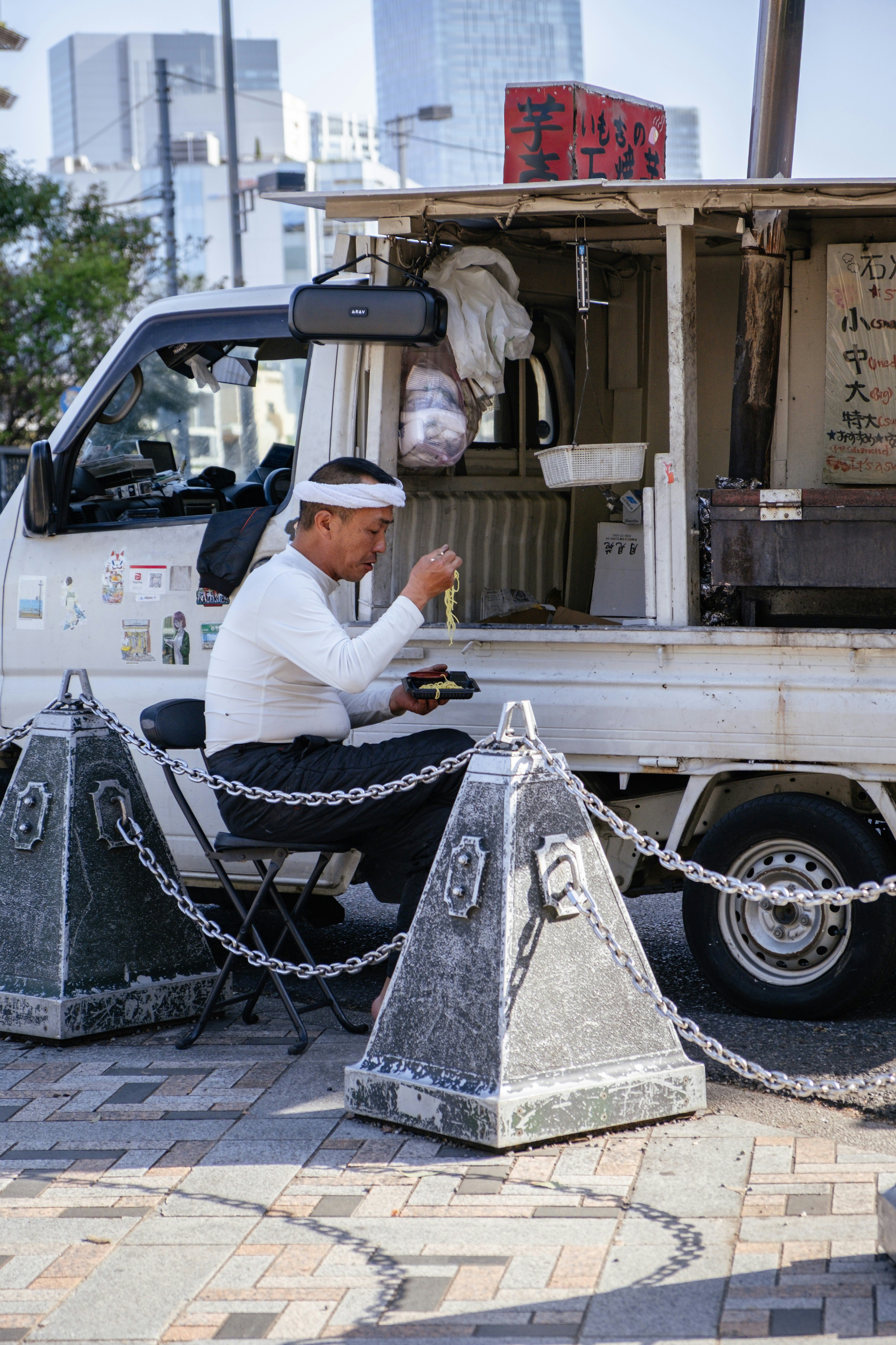 Street vendor enjoying a bowl of noodles outside a food truck in an urban setting. The scene captures the essence of local street food culture.