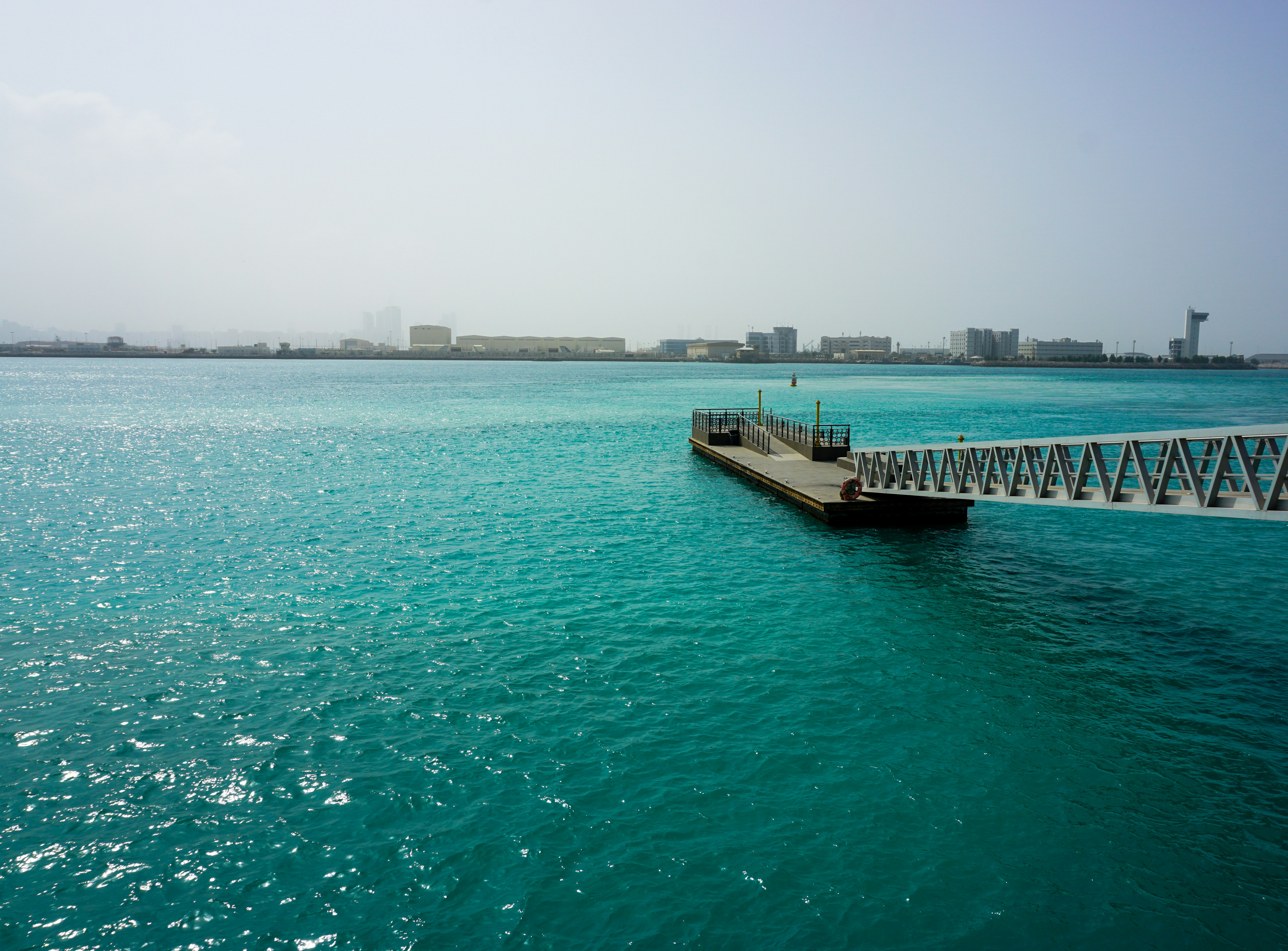 Wooden pier extending into vibrant turquoise waters under a hazy sky, showcasing a tranquil coastal scene.