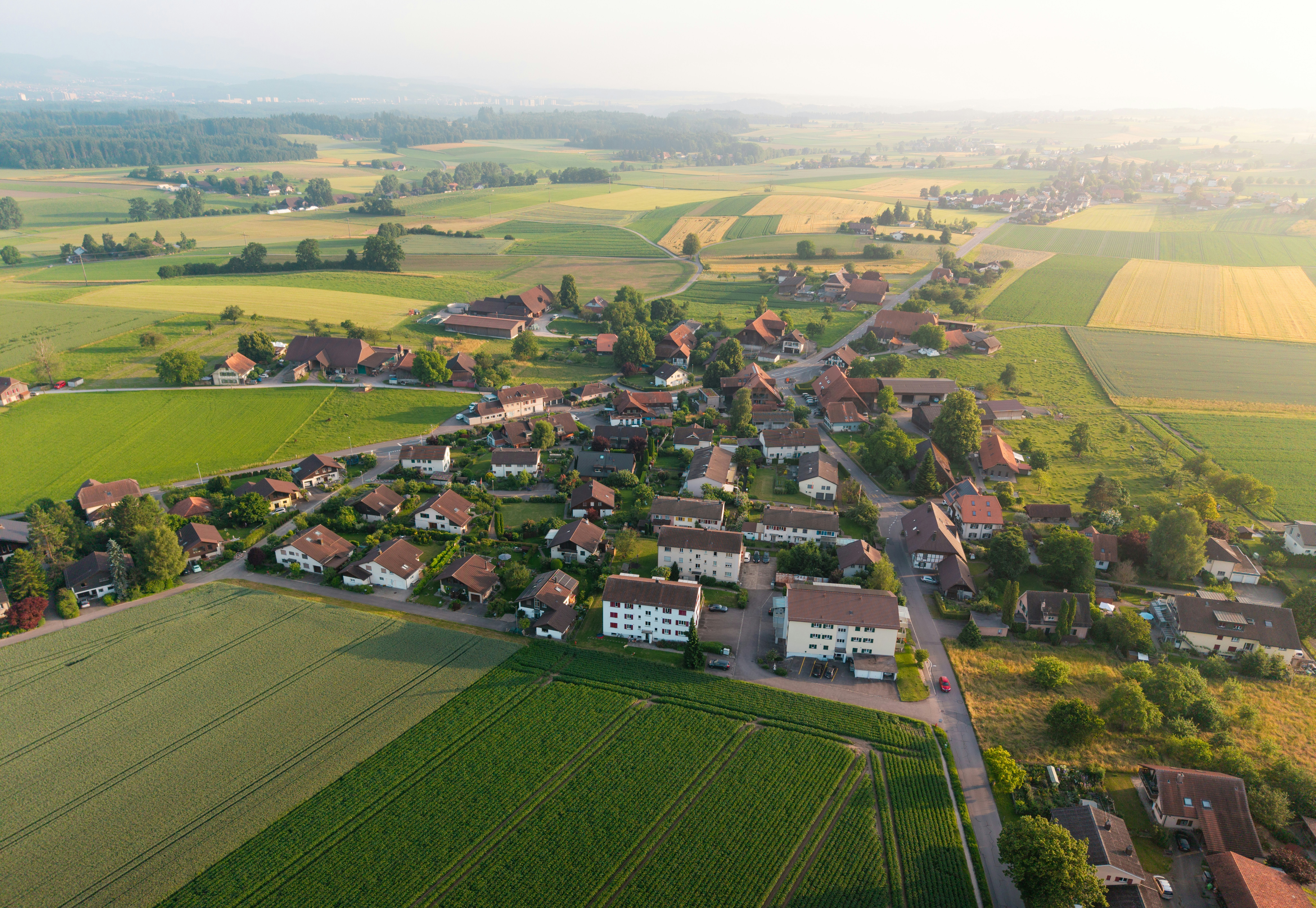 Aerial view of a quaint village surrounded by lush fields and patchwork farmland, showcasing the serene beauty of rural life.