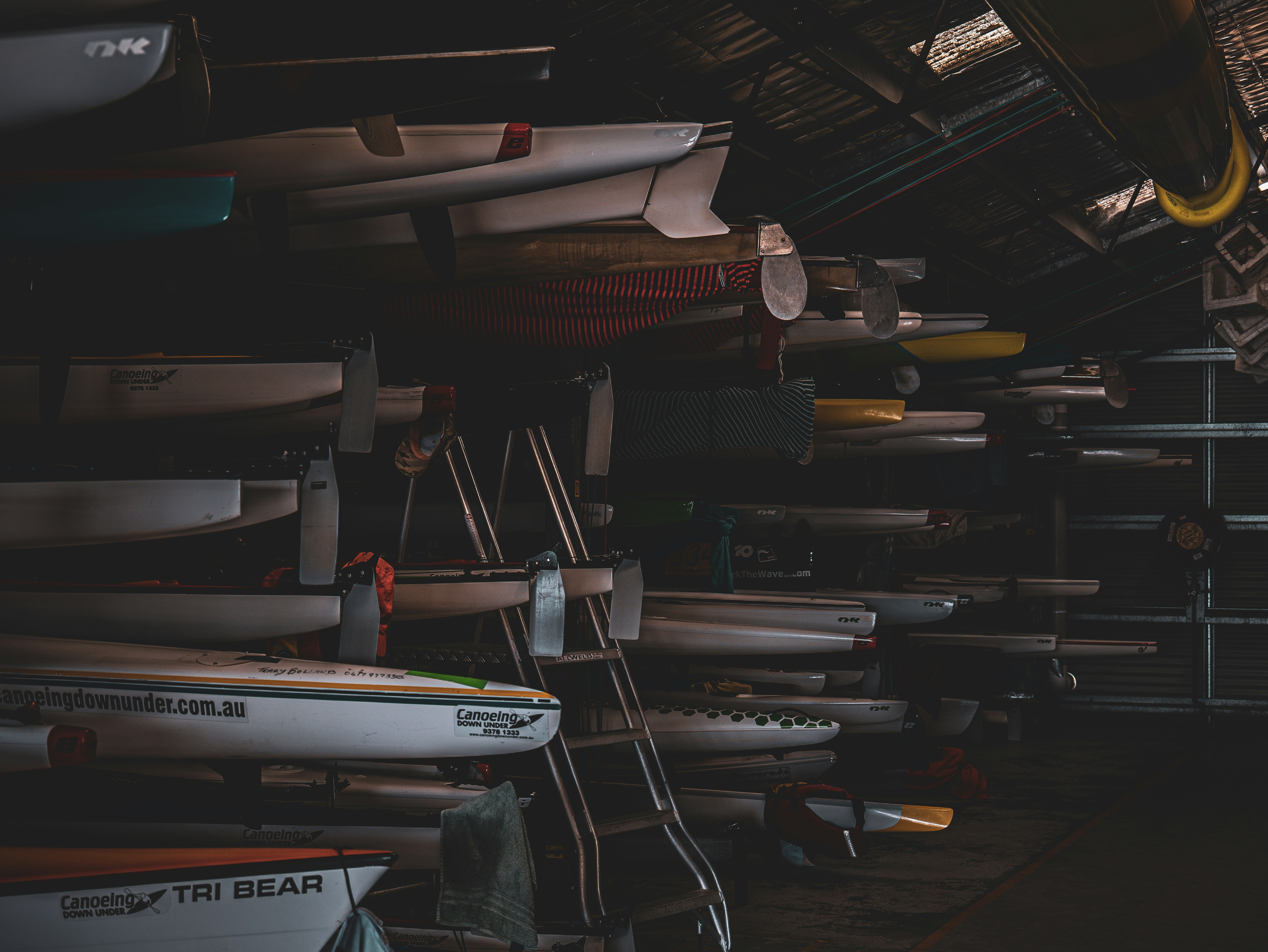 A dimly lit storage area filled with neatly arranged kayaks and canoes, showcasing their vibrant colors against the dark surroundings.