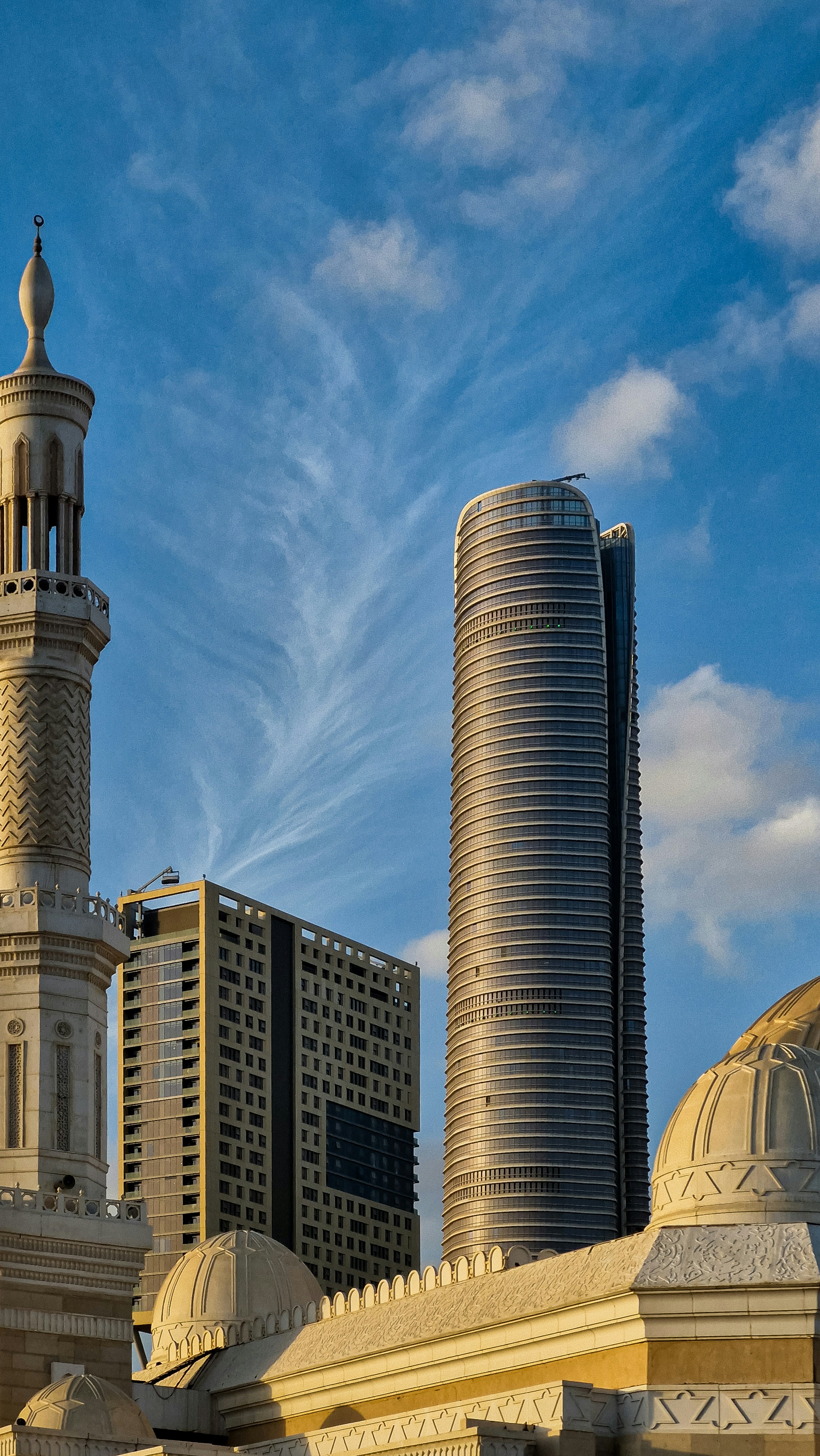A mosque and modern buildings under a blue sky.