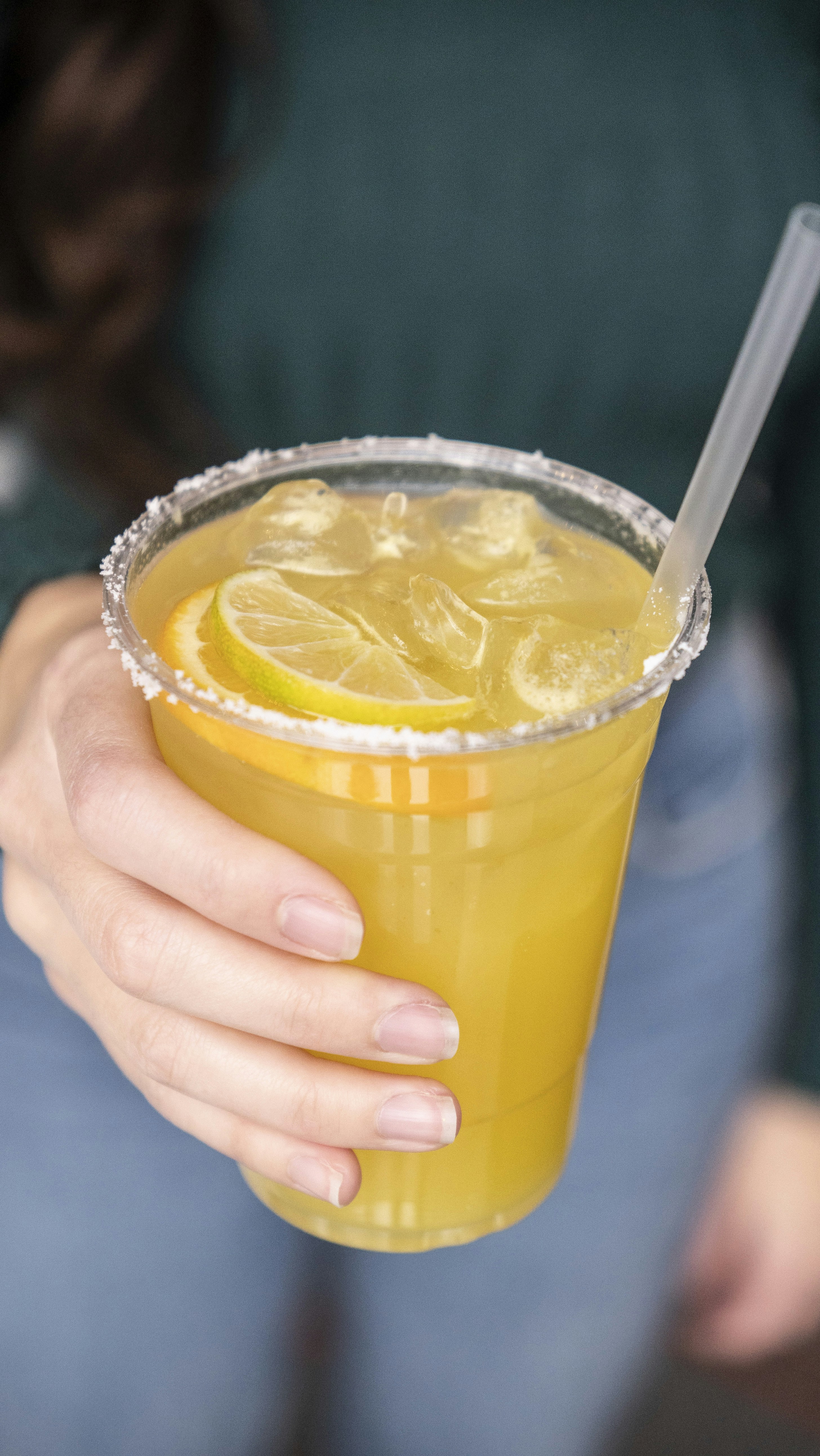 Refreshing yellow drink with citrus slices and ice, held by a person with a partially visible hand. The glass rim is adorned with salt.